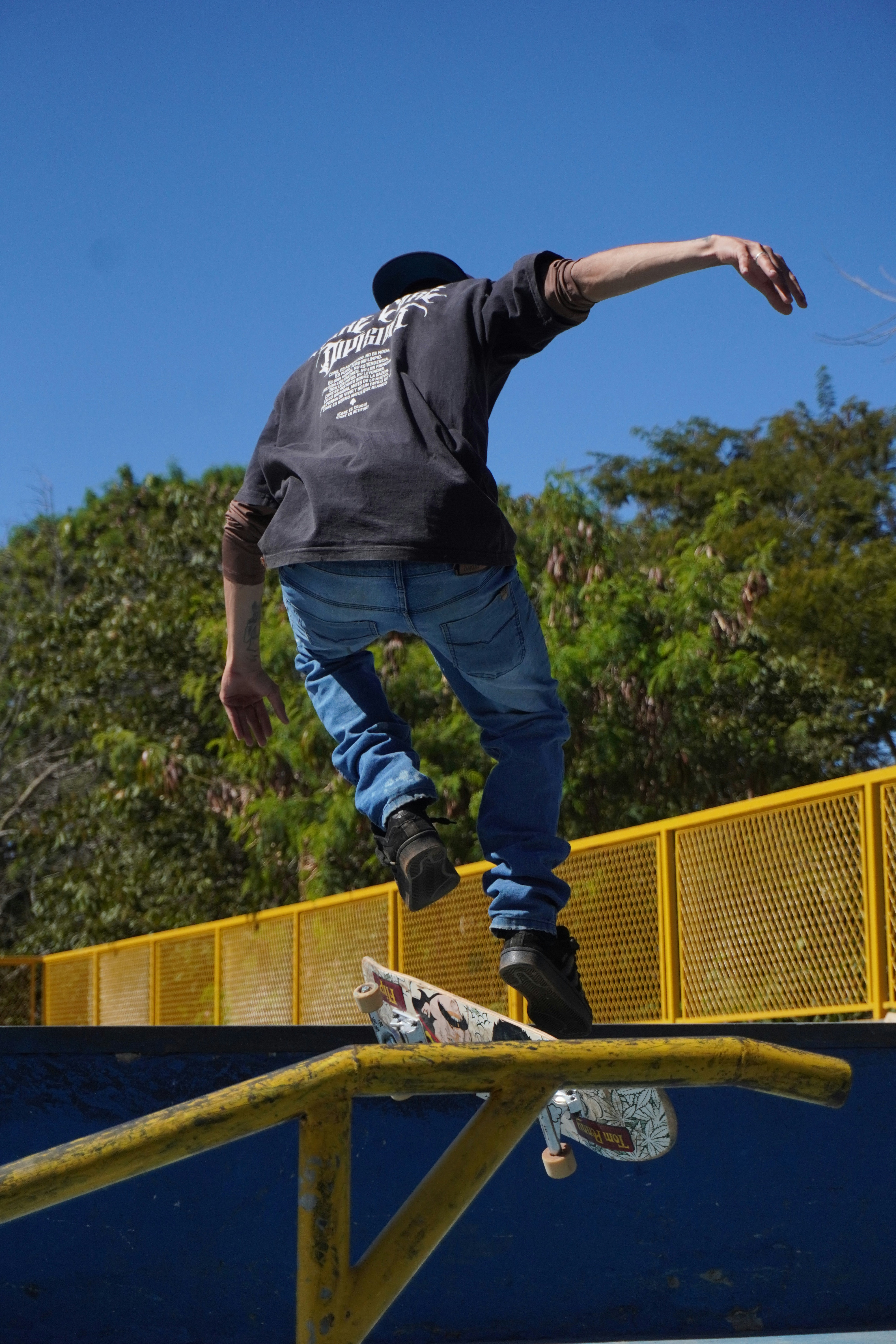 Skateboarder in mid-air over a yellow railing against a clear blue sky