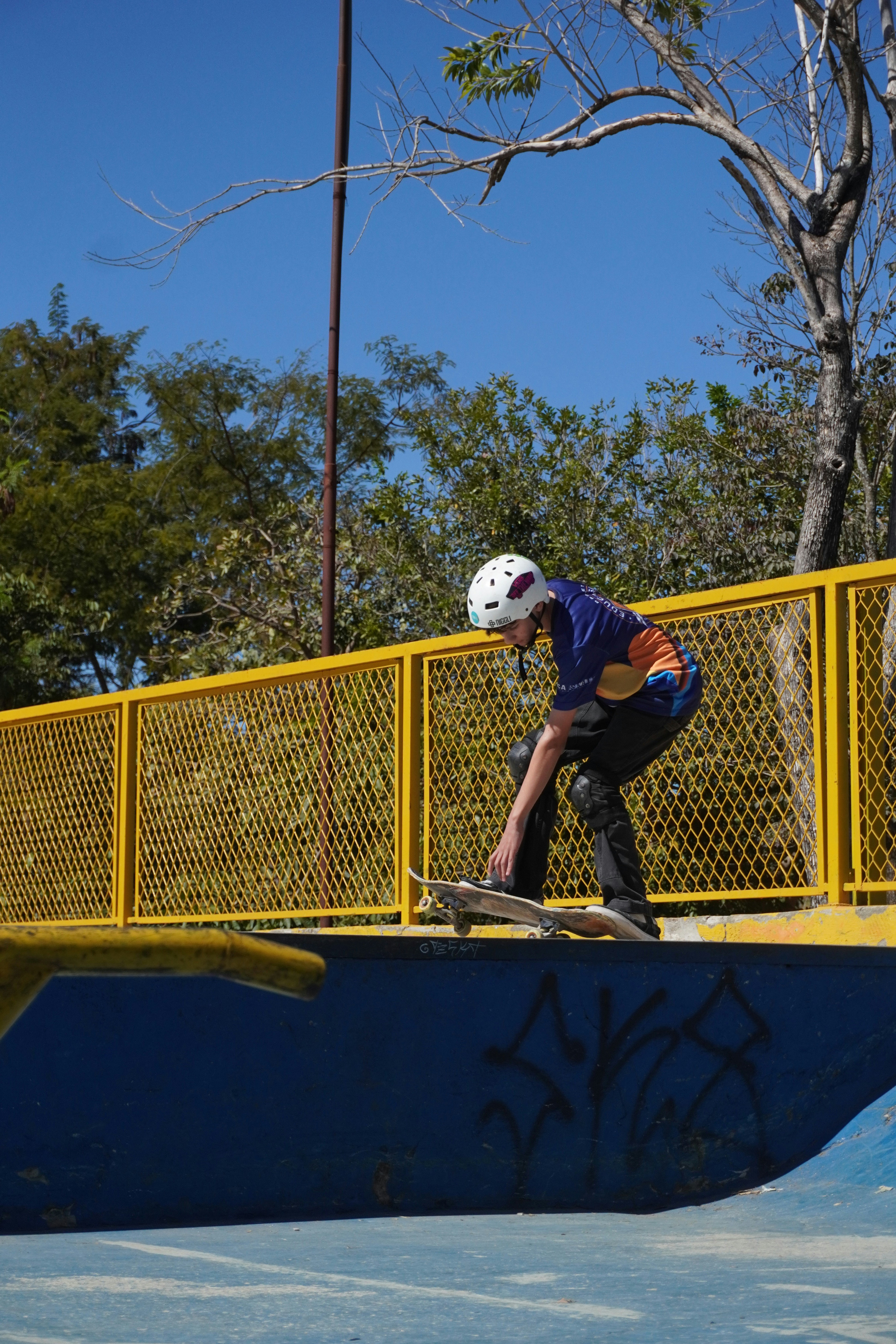 Skateboarder in mid-tilt over a graffitied bowl beneath a yellow railing