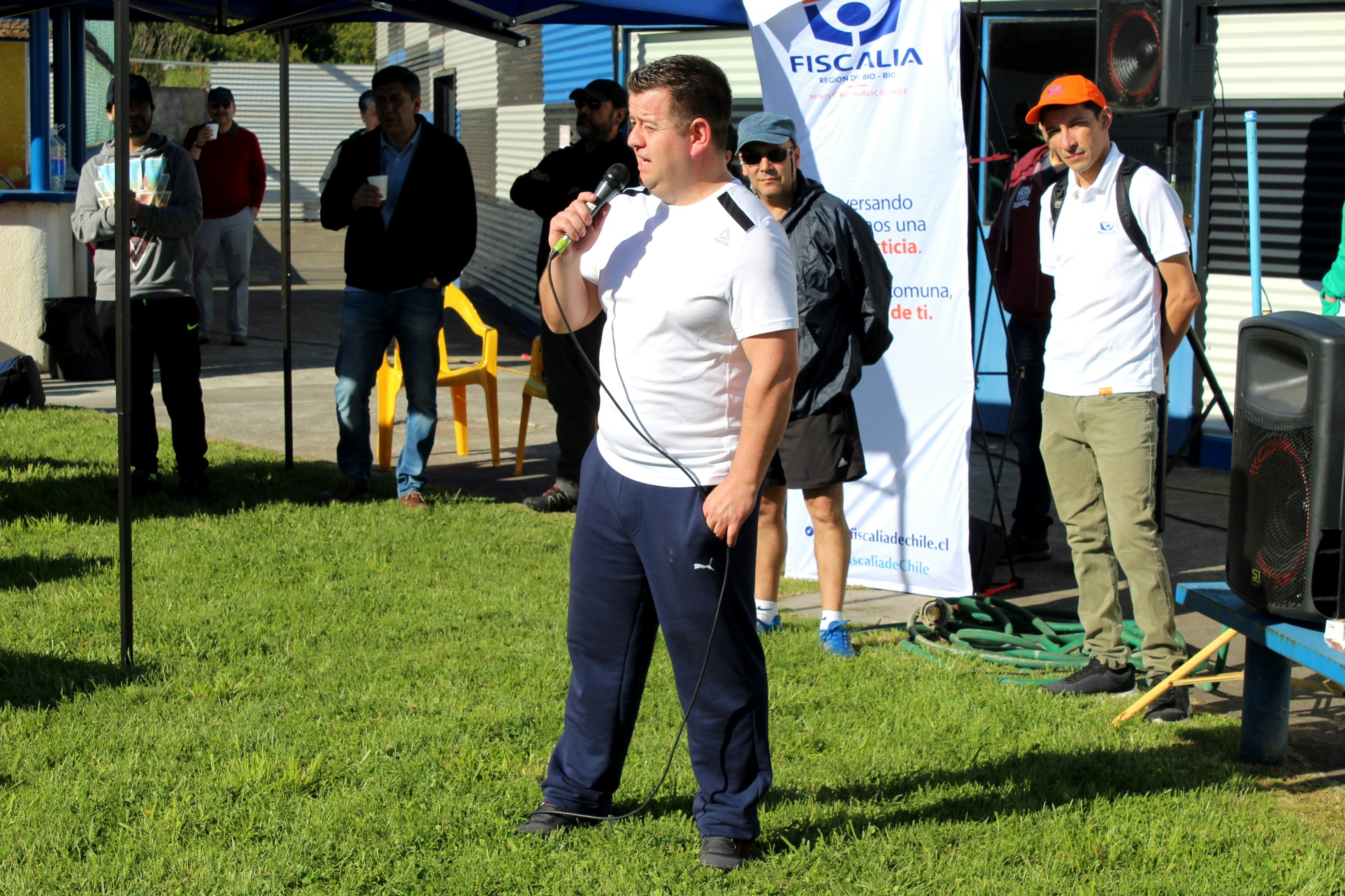 Outdoor speaker grips the mic under a bannered event canopy