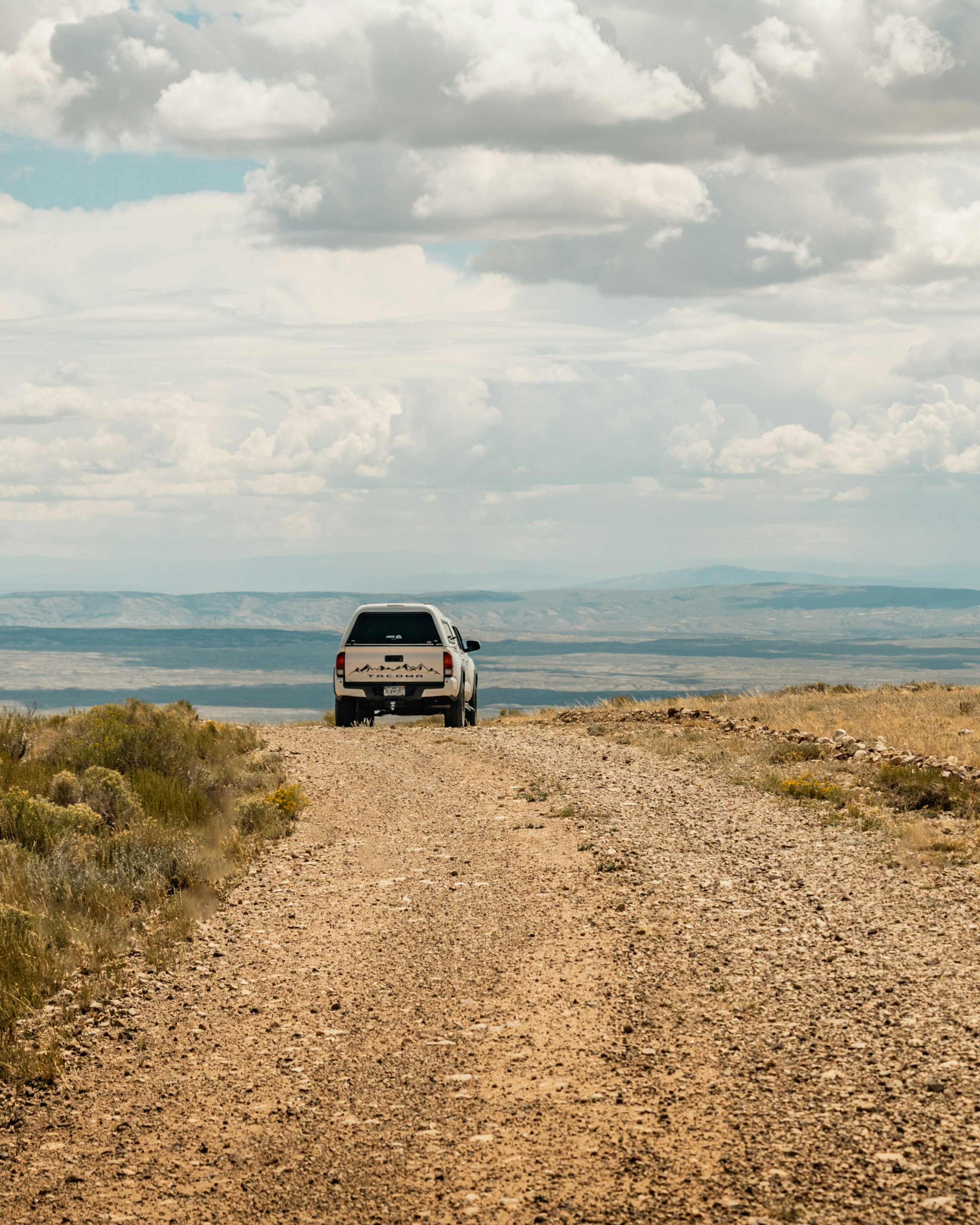 White pickup on a dusty desert road toward a distant lake and hills