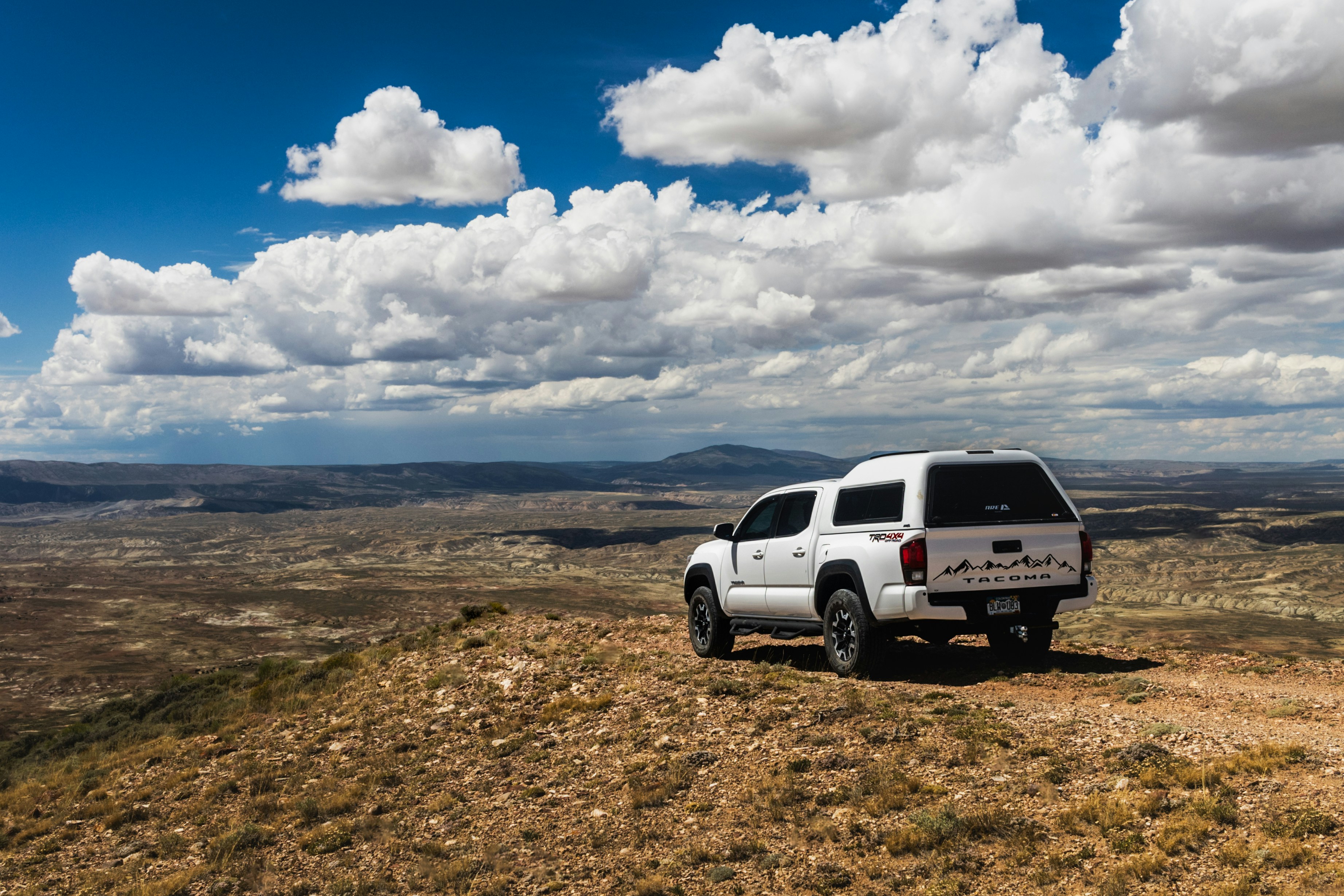 White pickup on a windswept canyon rim beneath a dramatic cloudscape