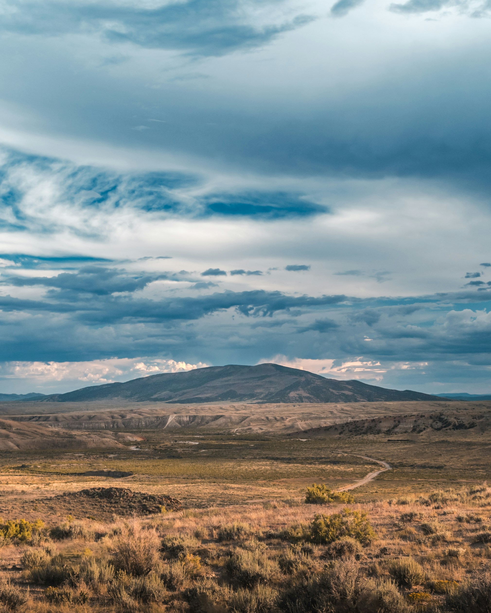 Dusty Road to the Mesa: A Quiet Desert Horizon Under Striated Clouds