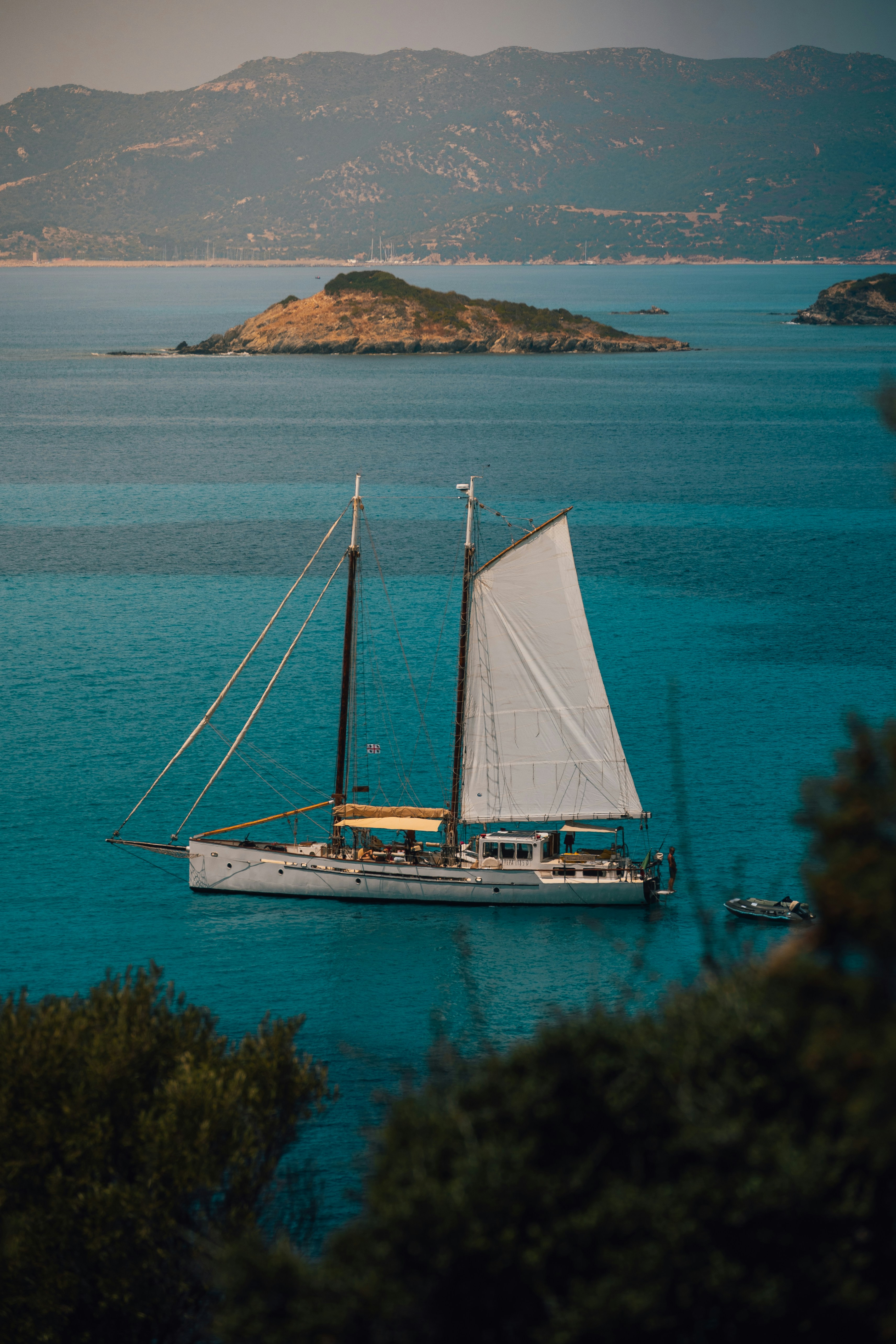 Sailing silhouette: a lone schooner anchors in turquoise coves beneath distant mountains