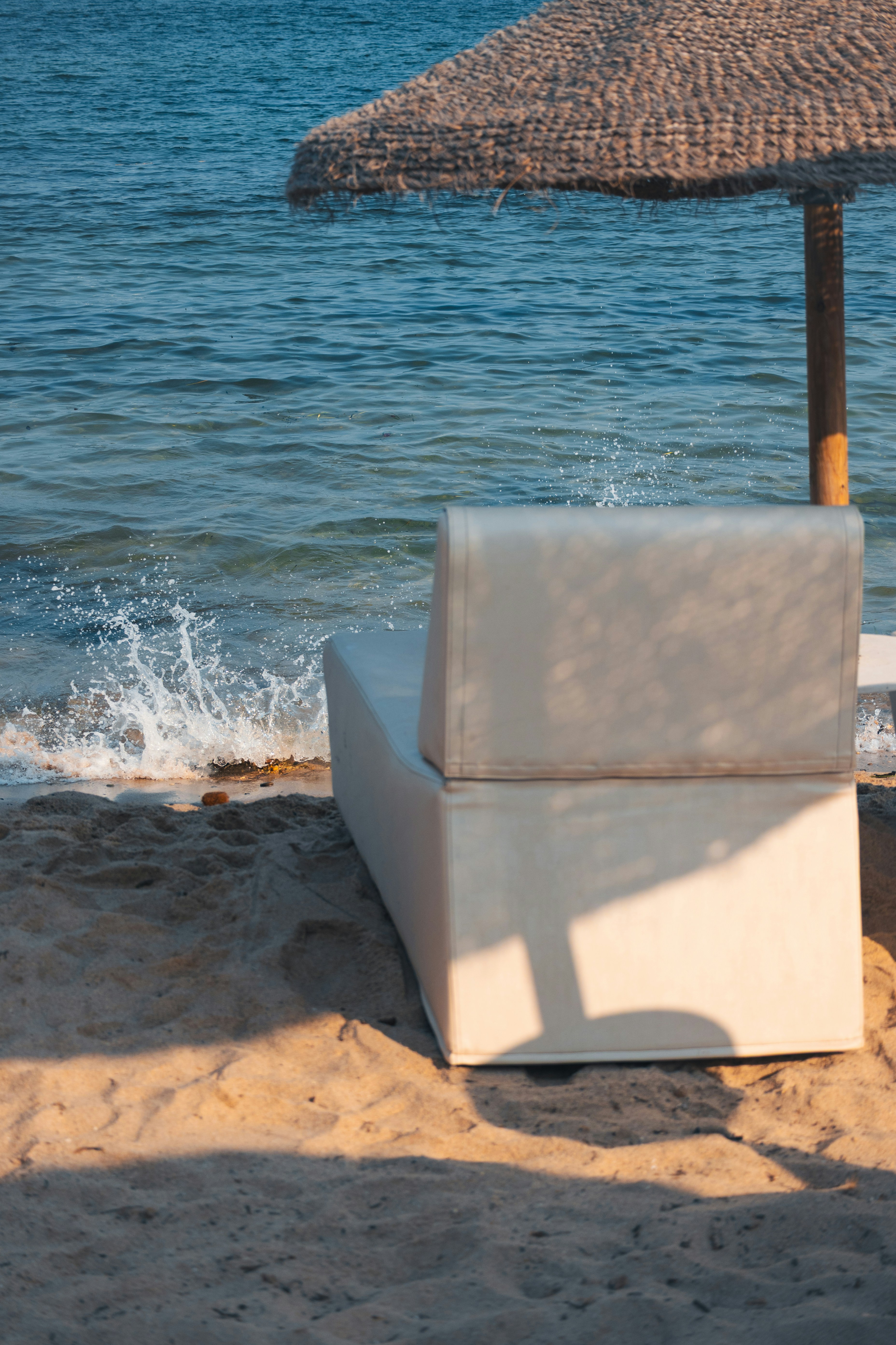 Sunlit Lounge by the Sea: A White Couch Under a Thatch Shade