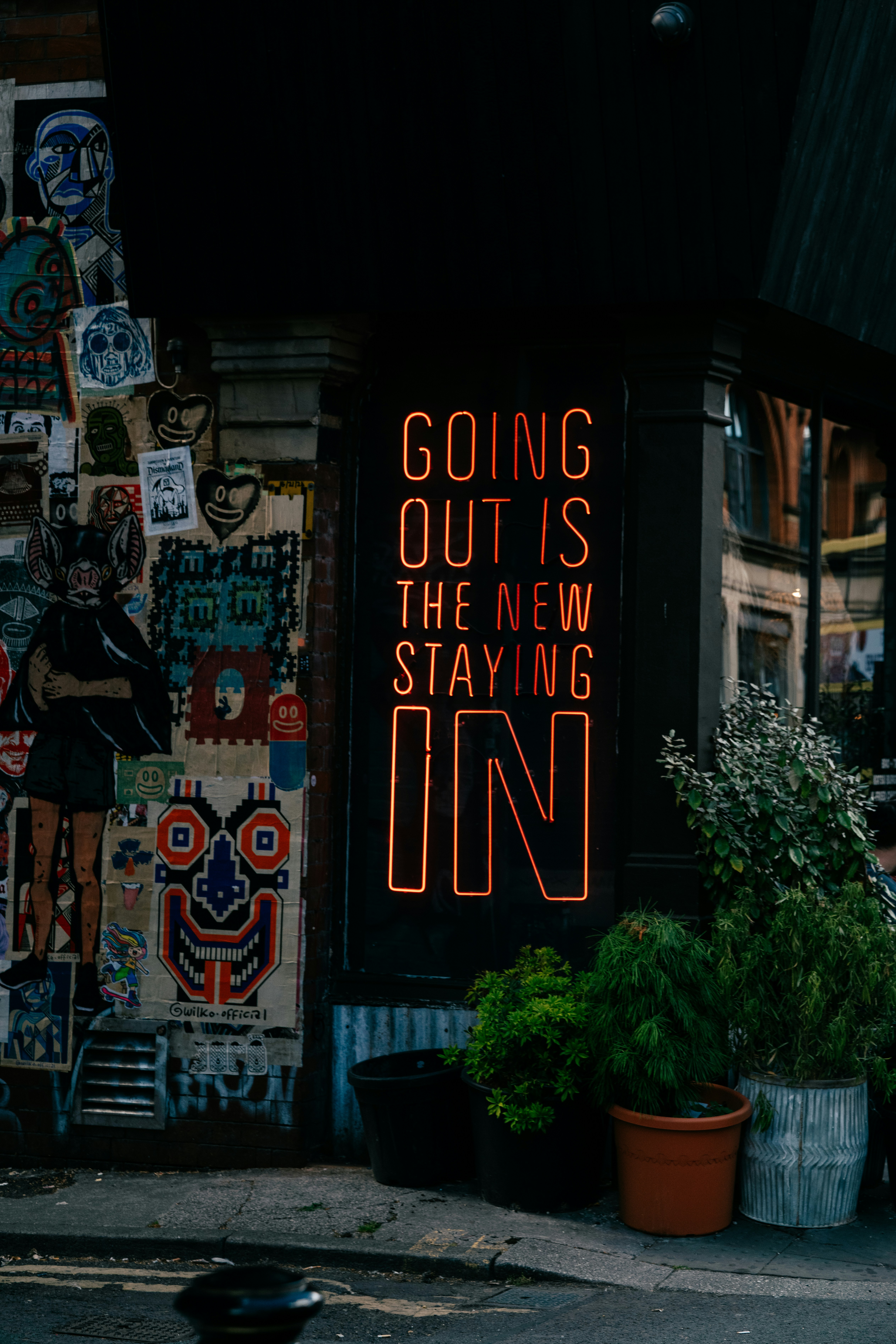 Neon Sign, Graffiti Wall, and Potted Greens Outside a City Venue