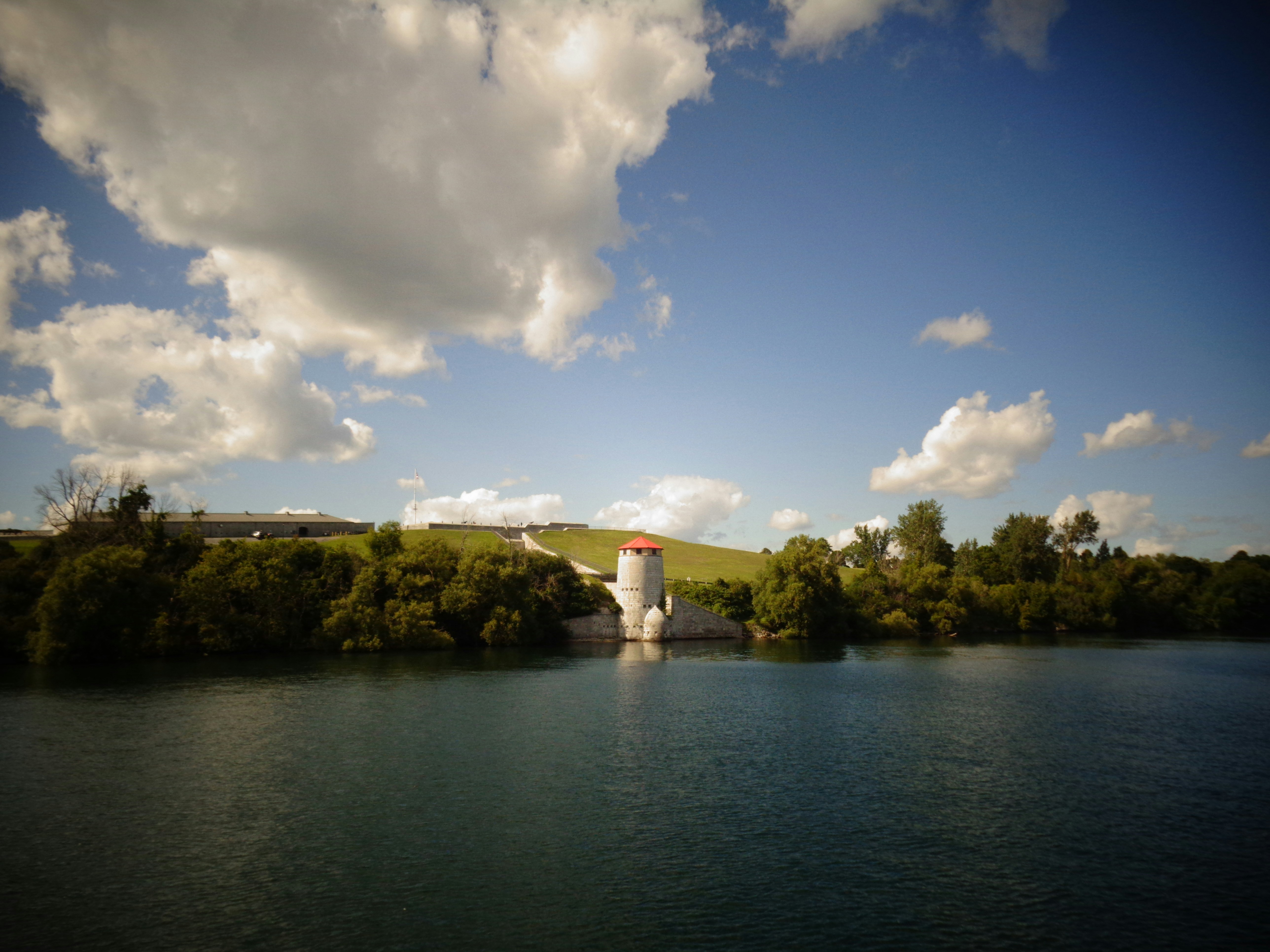Lighthouse among riverbank trees under a sculpted cloudscape