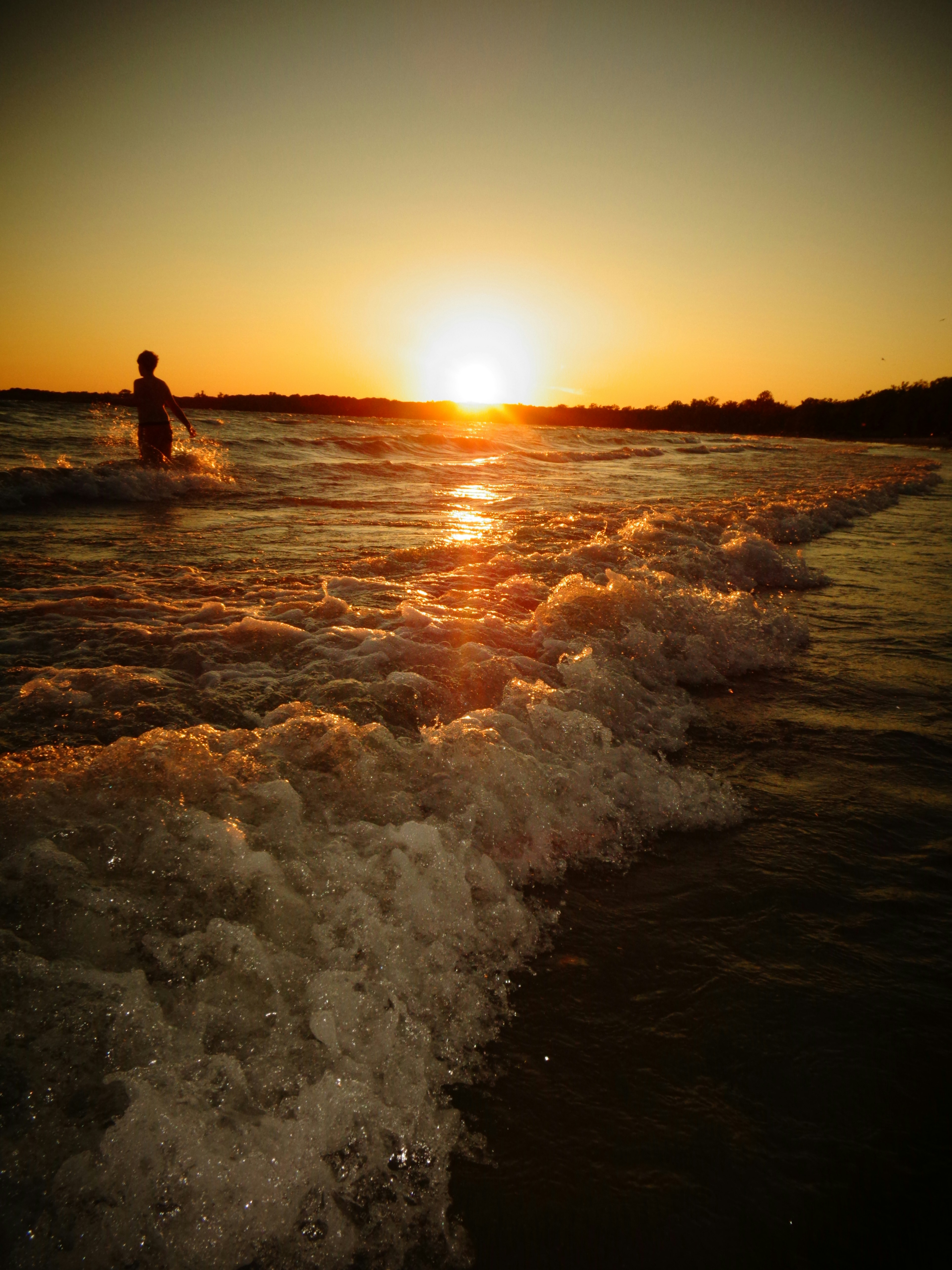 Sunlit Shoreline: A Lone Figure Traverses the Cresting Waves at Sunset