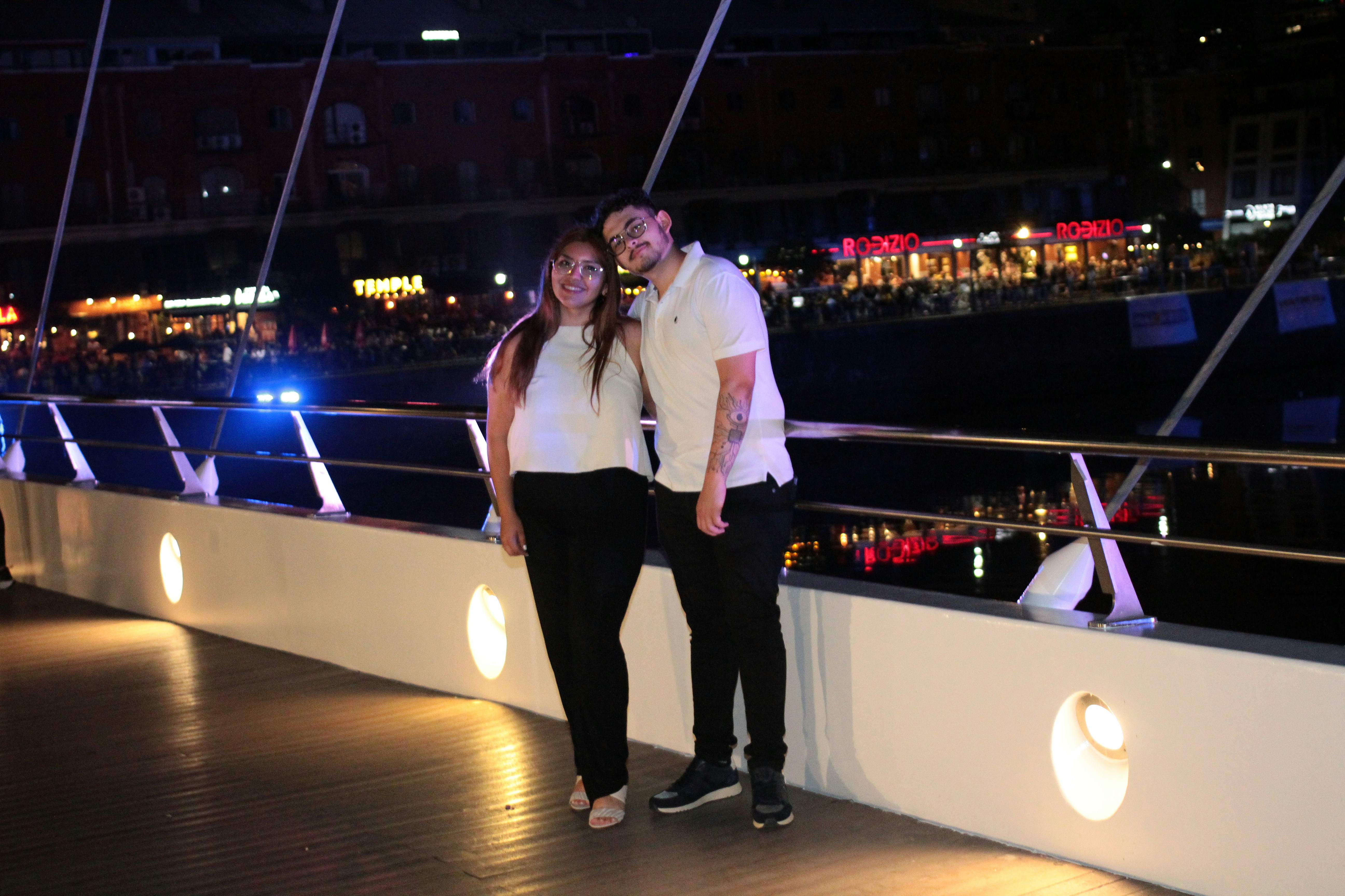 Night duet on the quay: a couple leaning into the city glow
