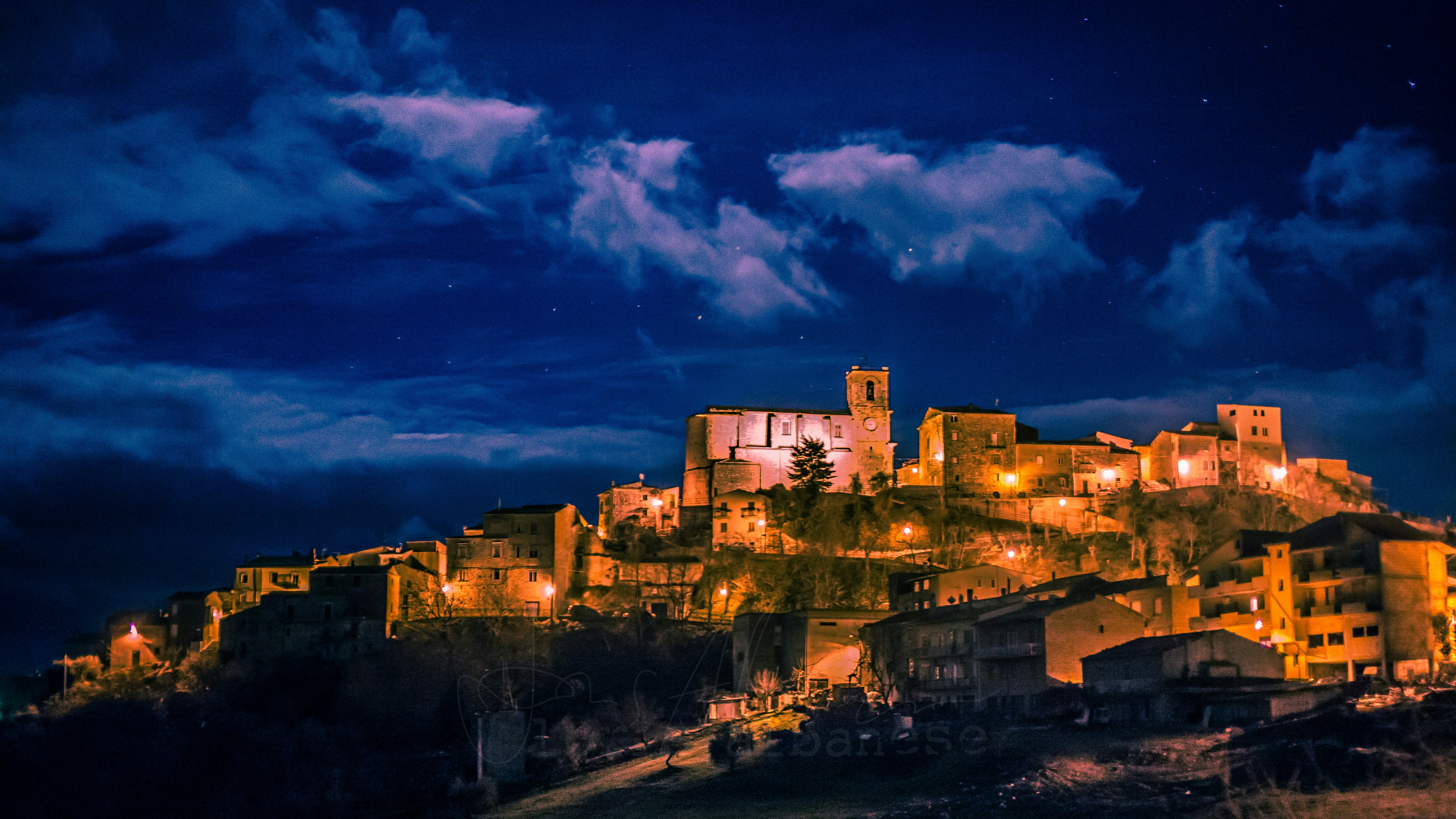 Illuminated hill fortress under a starry velocity of clouds