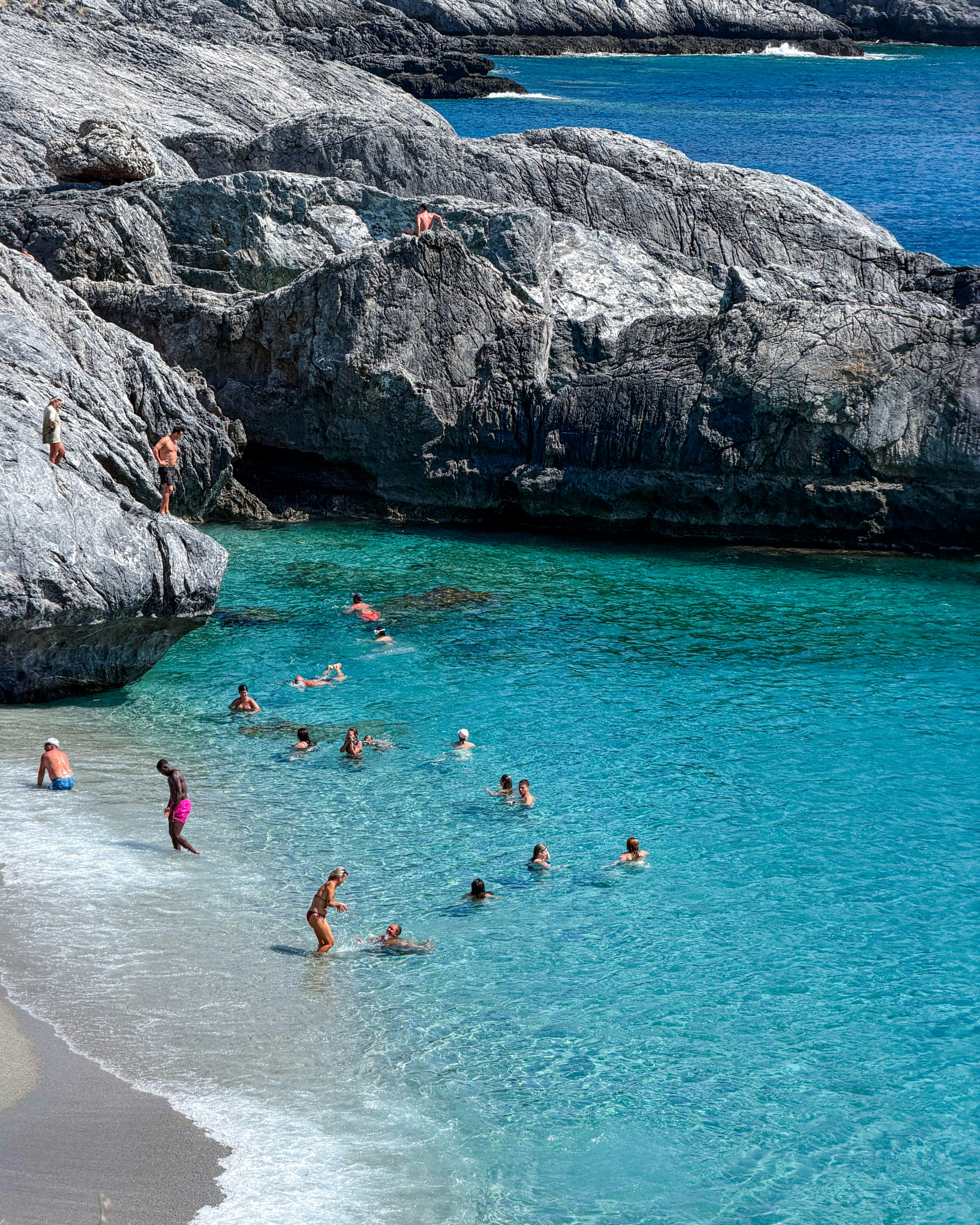 Sunlit Cove: People Enjoying Turquoise Waters Among Rugged Granite