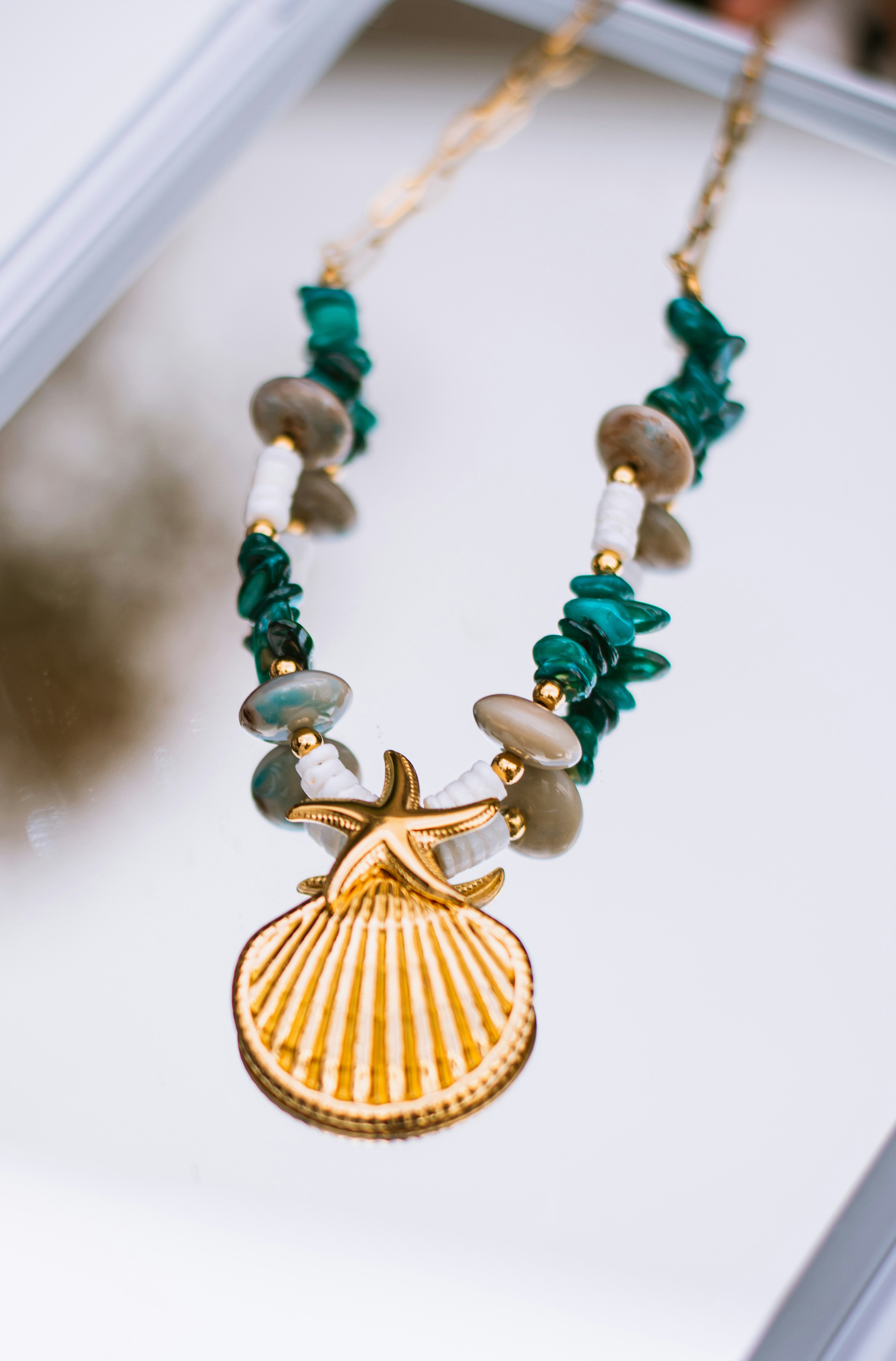 Coastal Charm: a turquoise bead necklace with a gold seashell pendant resting on a white tray