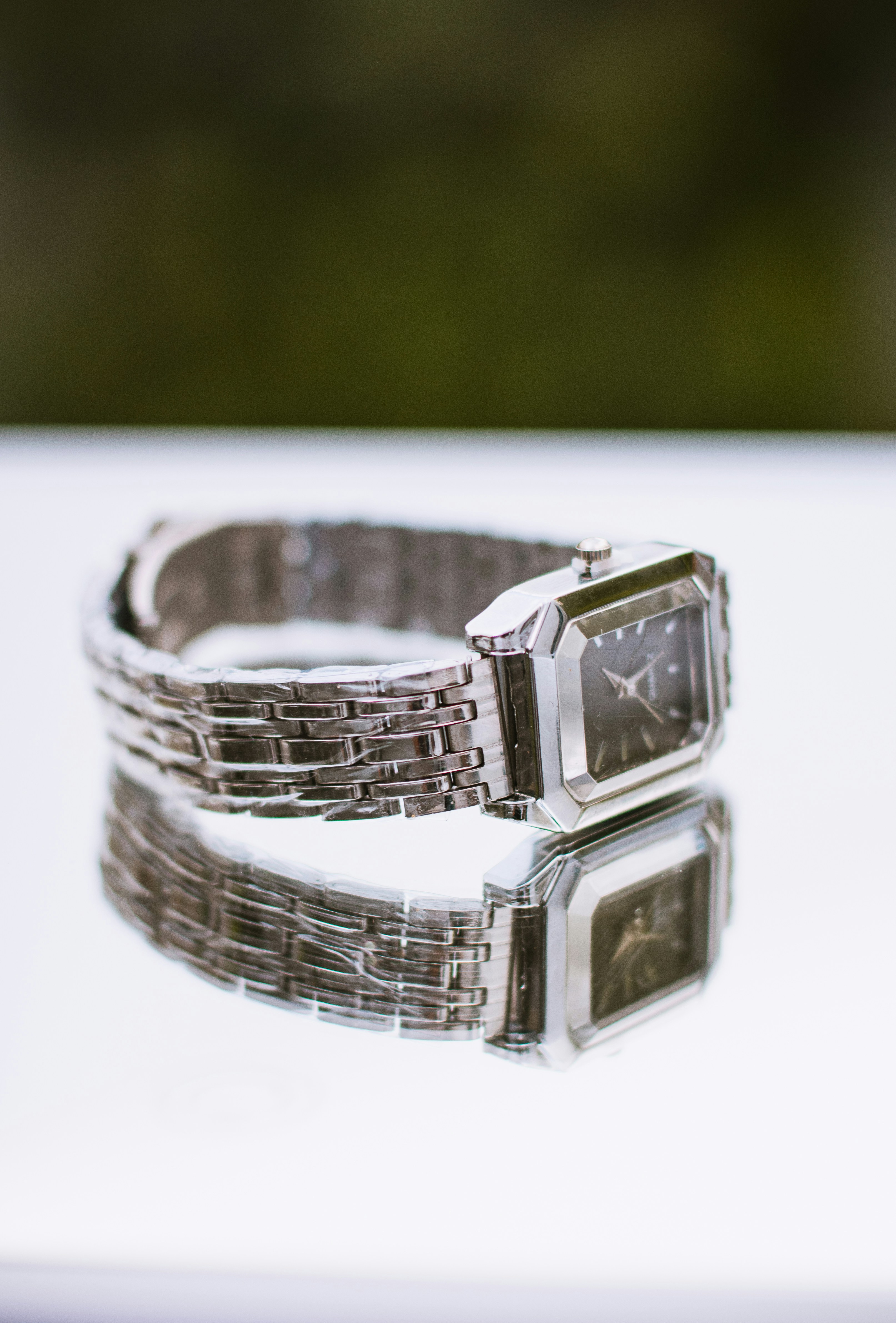 Reflected Precision: a silver wristwatch resting on glass and mirrored surface