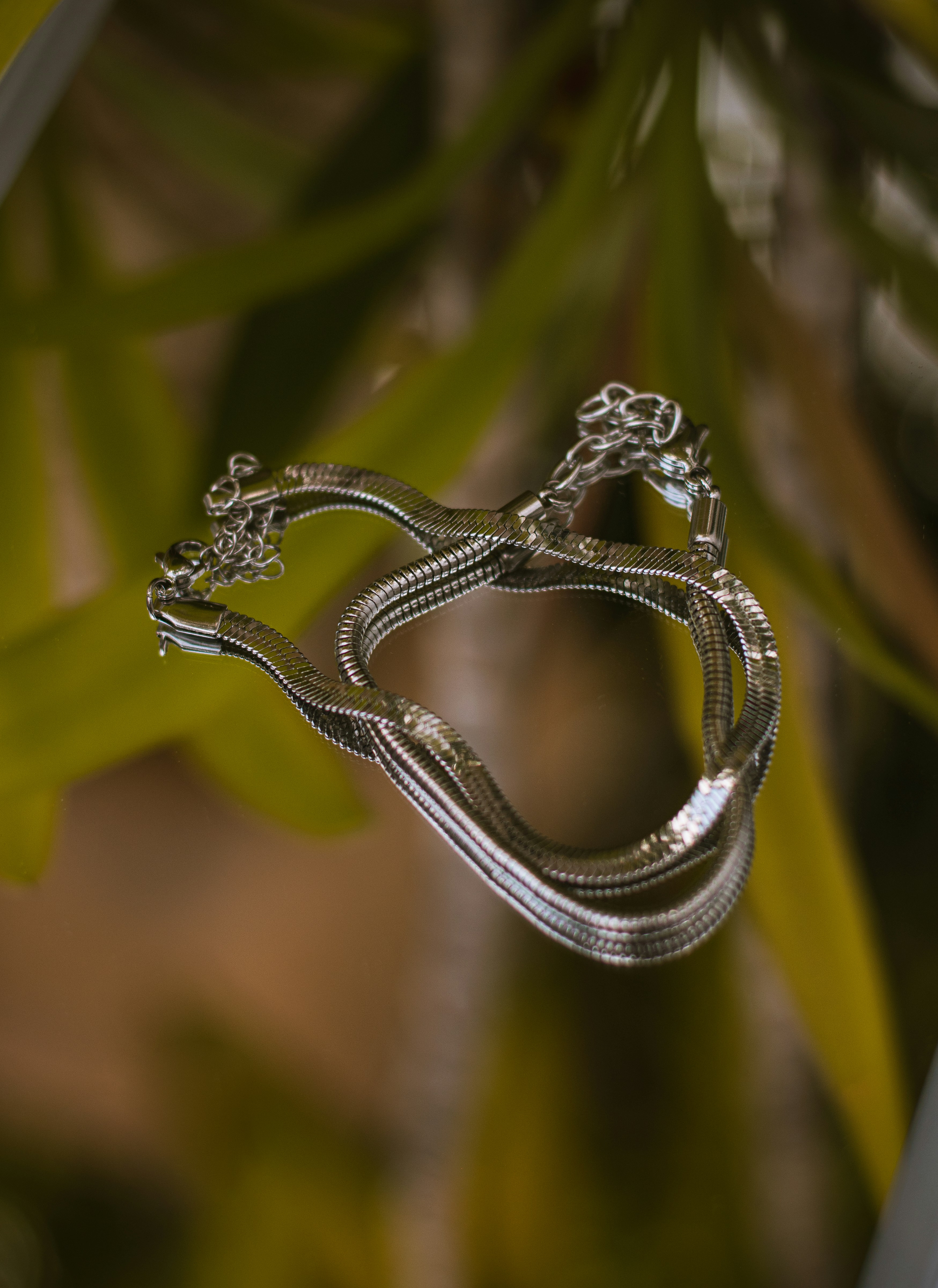 Coiled silver bracelets suspended in a tropical blur