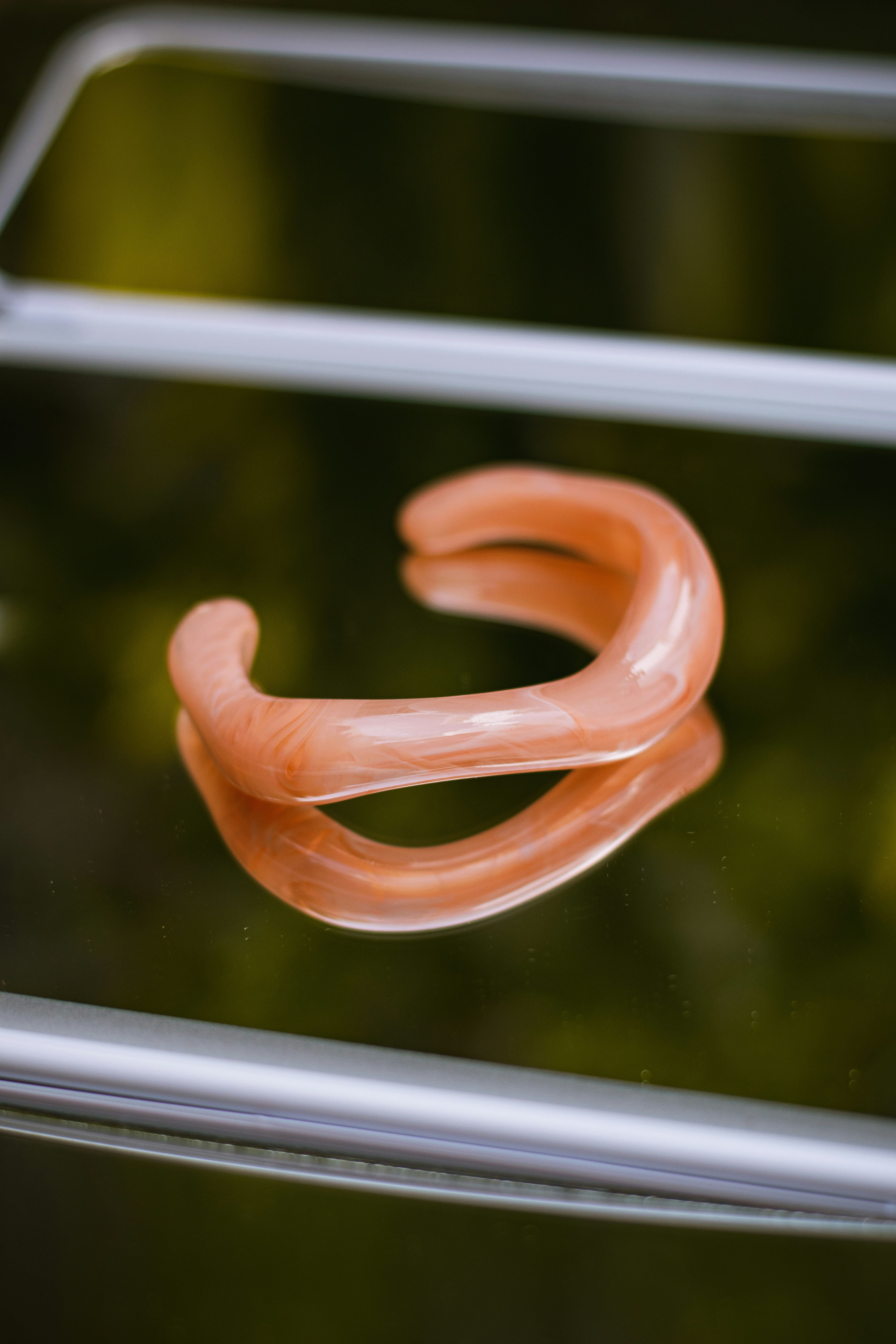 Curved Glass Reflections: A Soft Pink Loop on a Metallic Surface