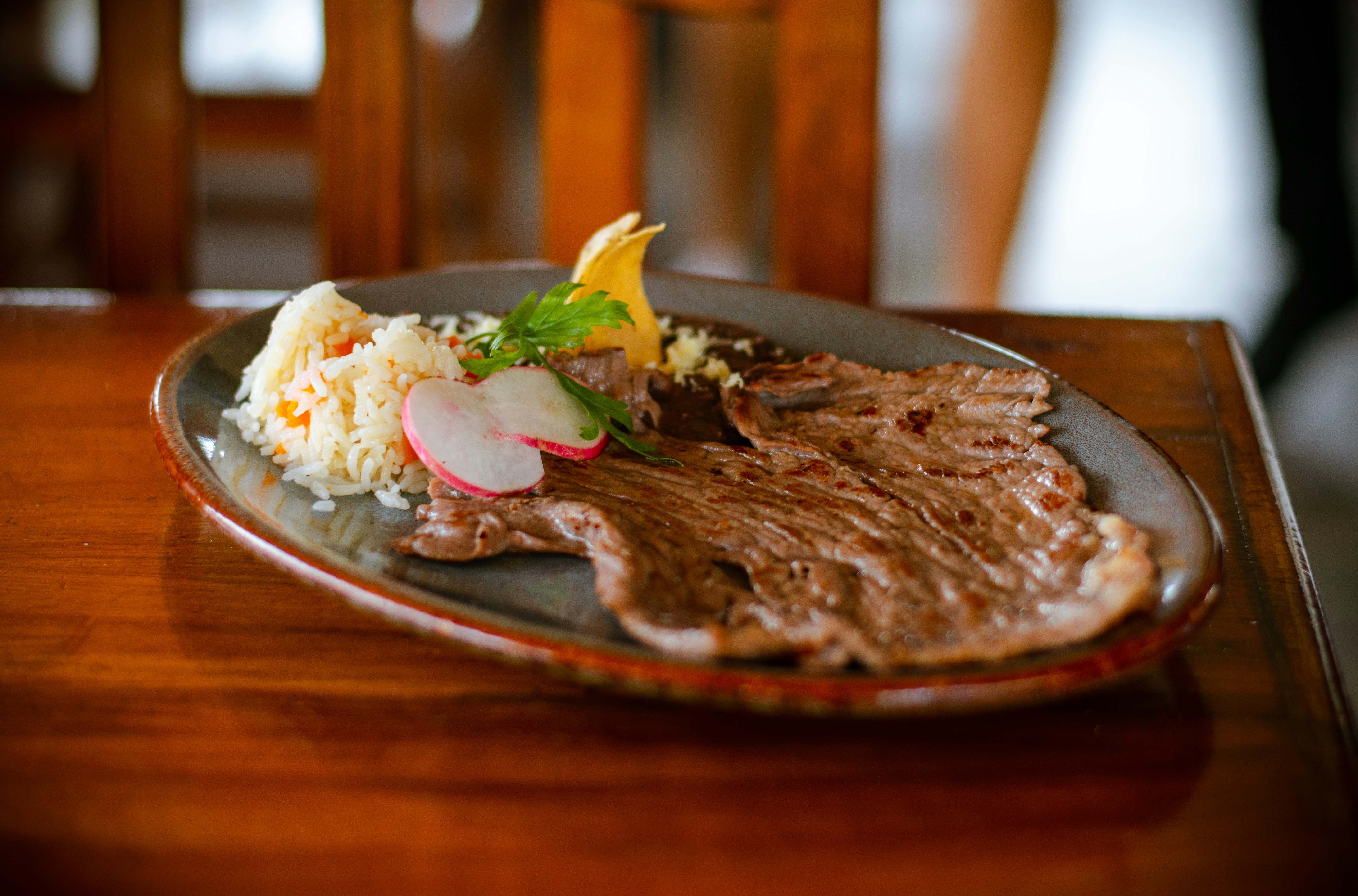 Grilled meat, rice, radish, and lime on a wooden table.