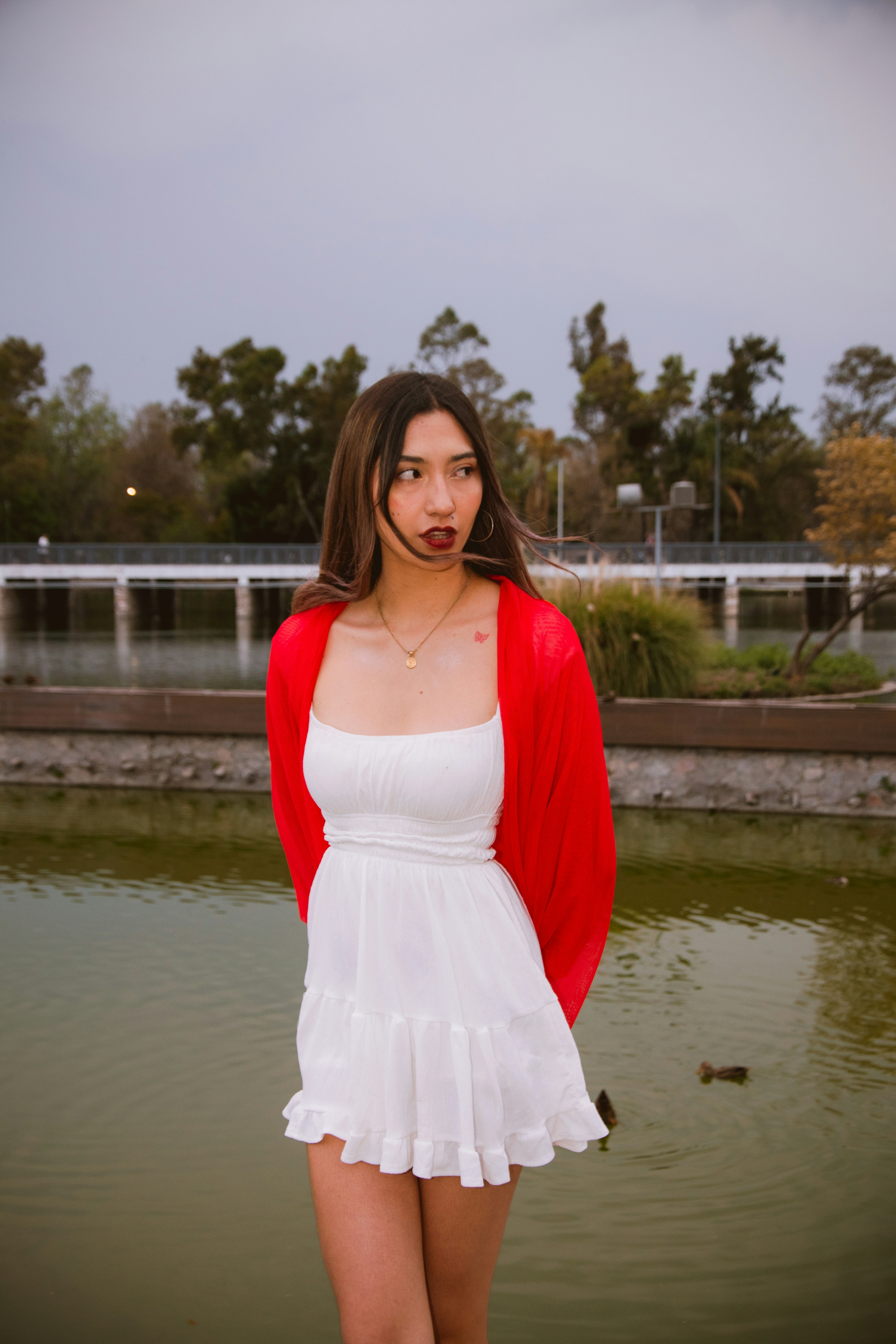 Red cardigan, white dress, and a lakeside gaze