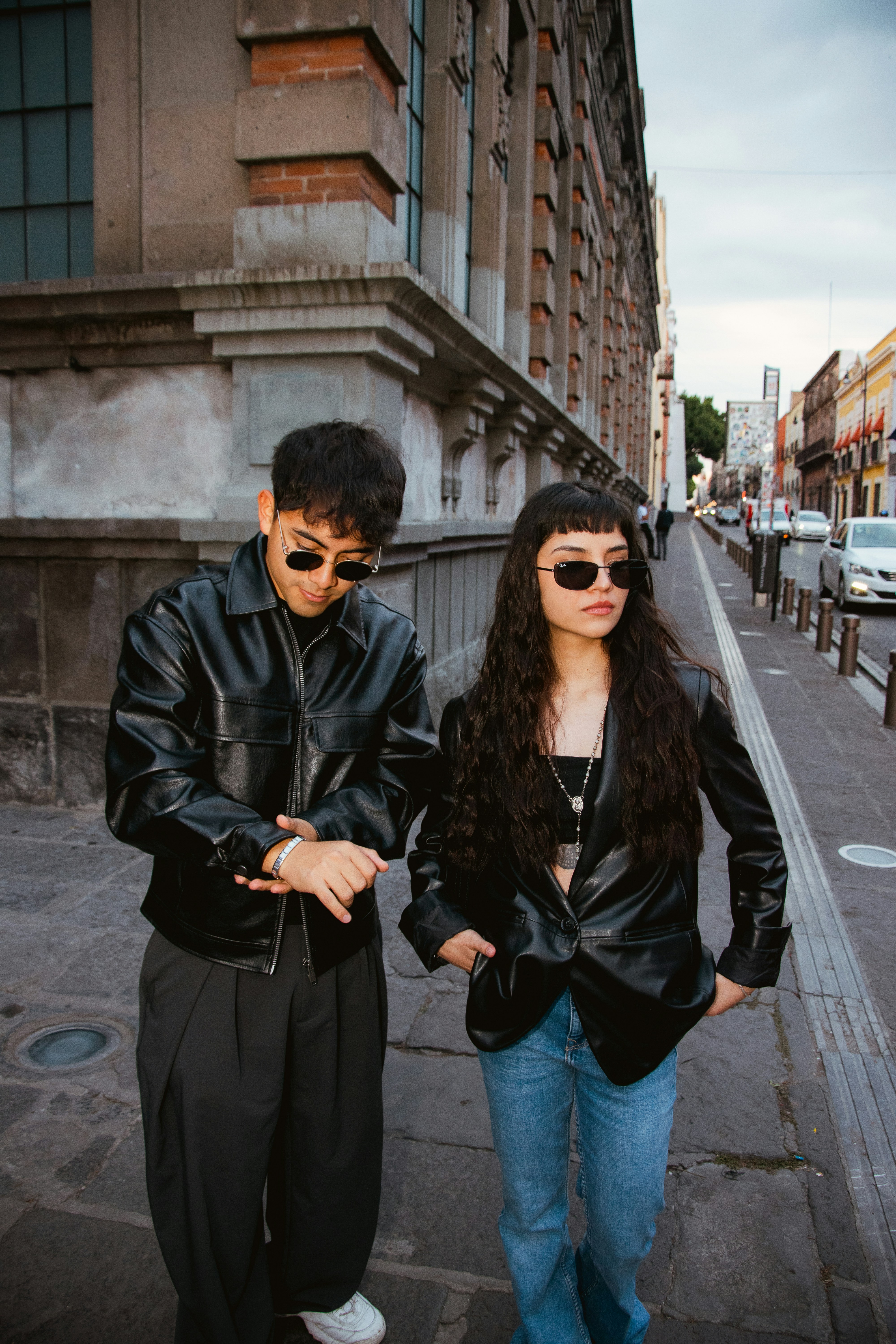 Street-styled duo in black leather glow along a cobblestone avenue