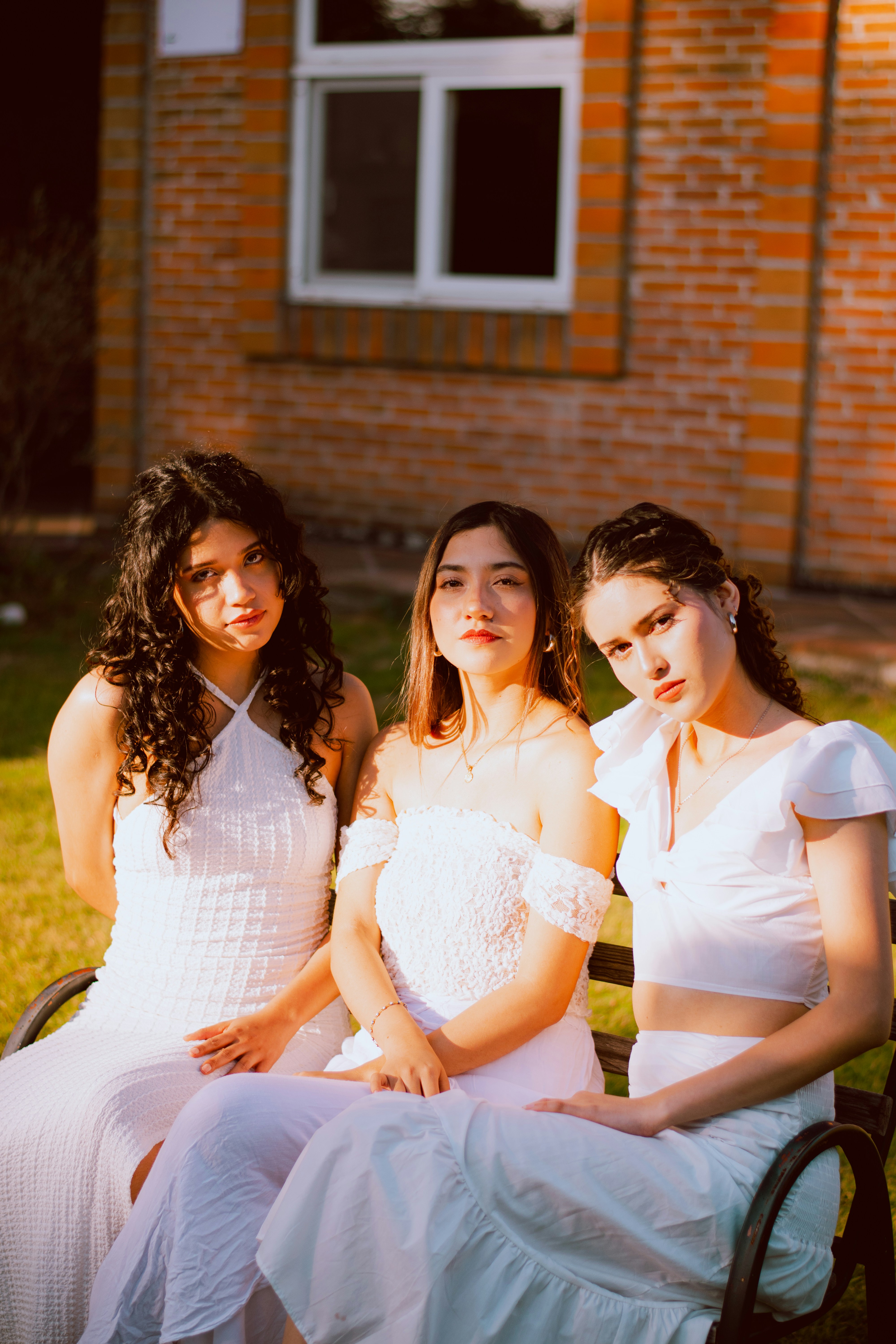 Three young women in white dresses sitting on a bench.