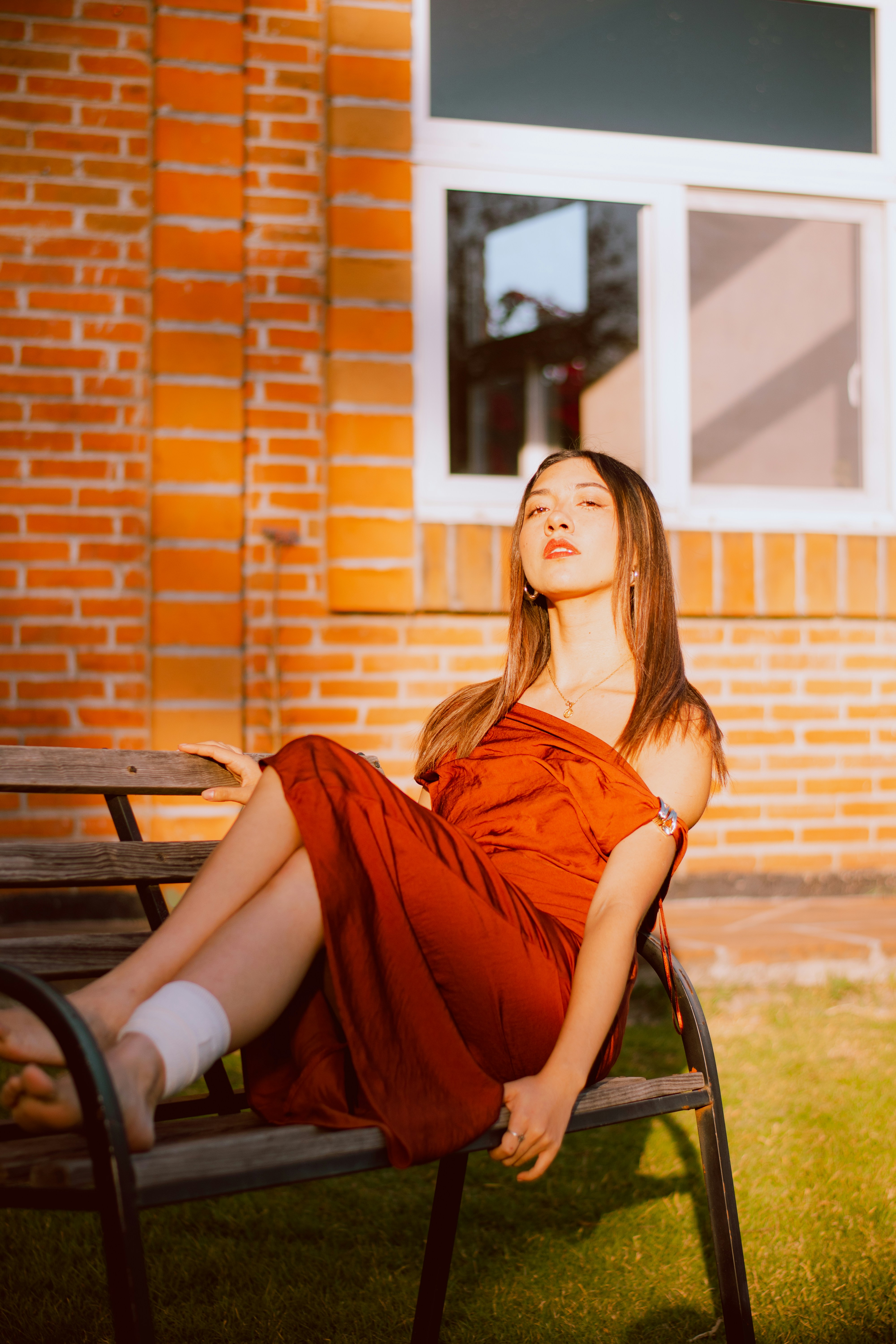 Sunlit Confidence: A Woman in a Rustic Red Dress on a Park Bench