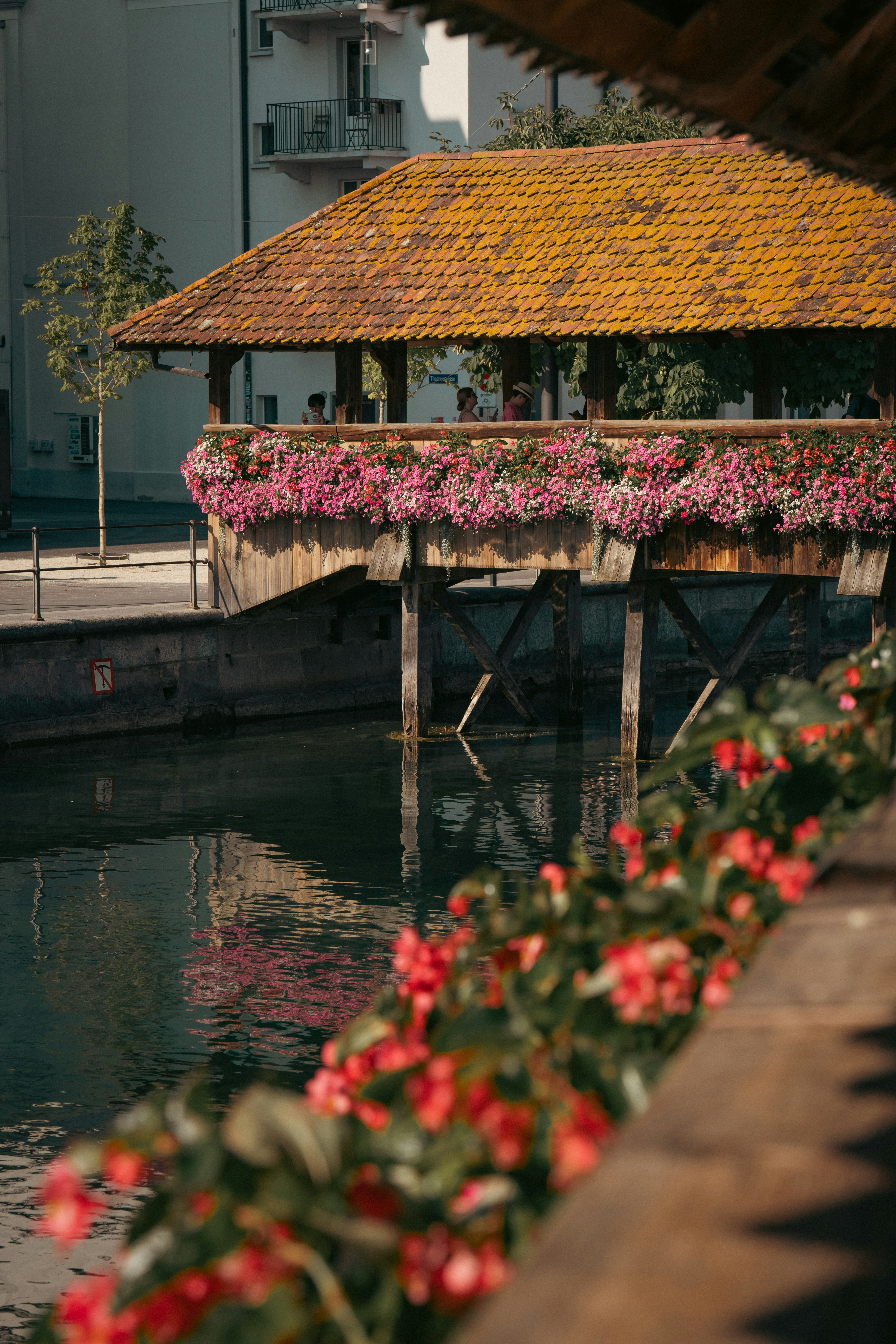 Flowered Wooden Bridge Over Calm Water in Sunlit Town