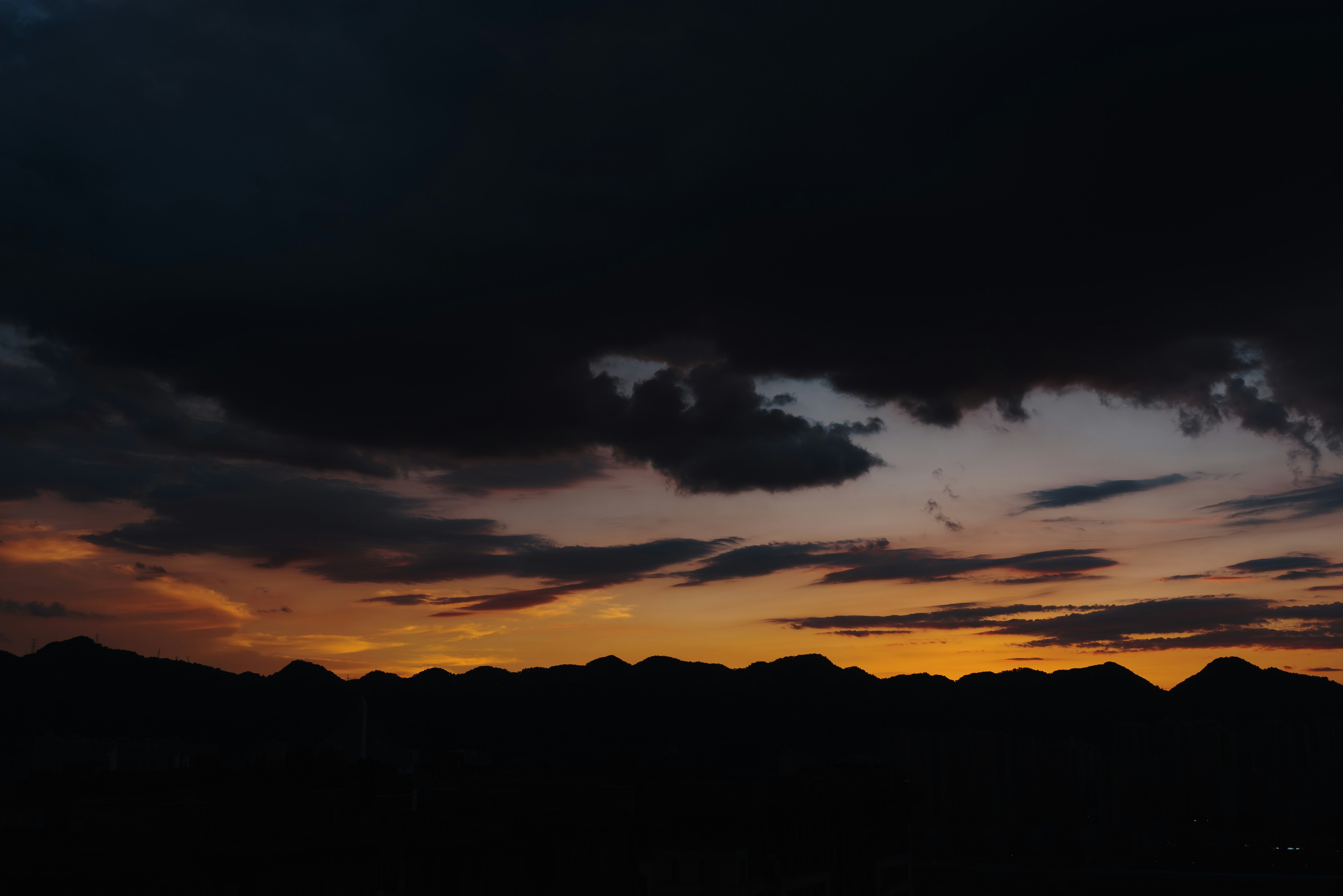 Silhouetted mountain range at sunset with a warm orange glow along the horizon; a calm, low-light landscape composition showcases a darkened sky and distant terrain.