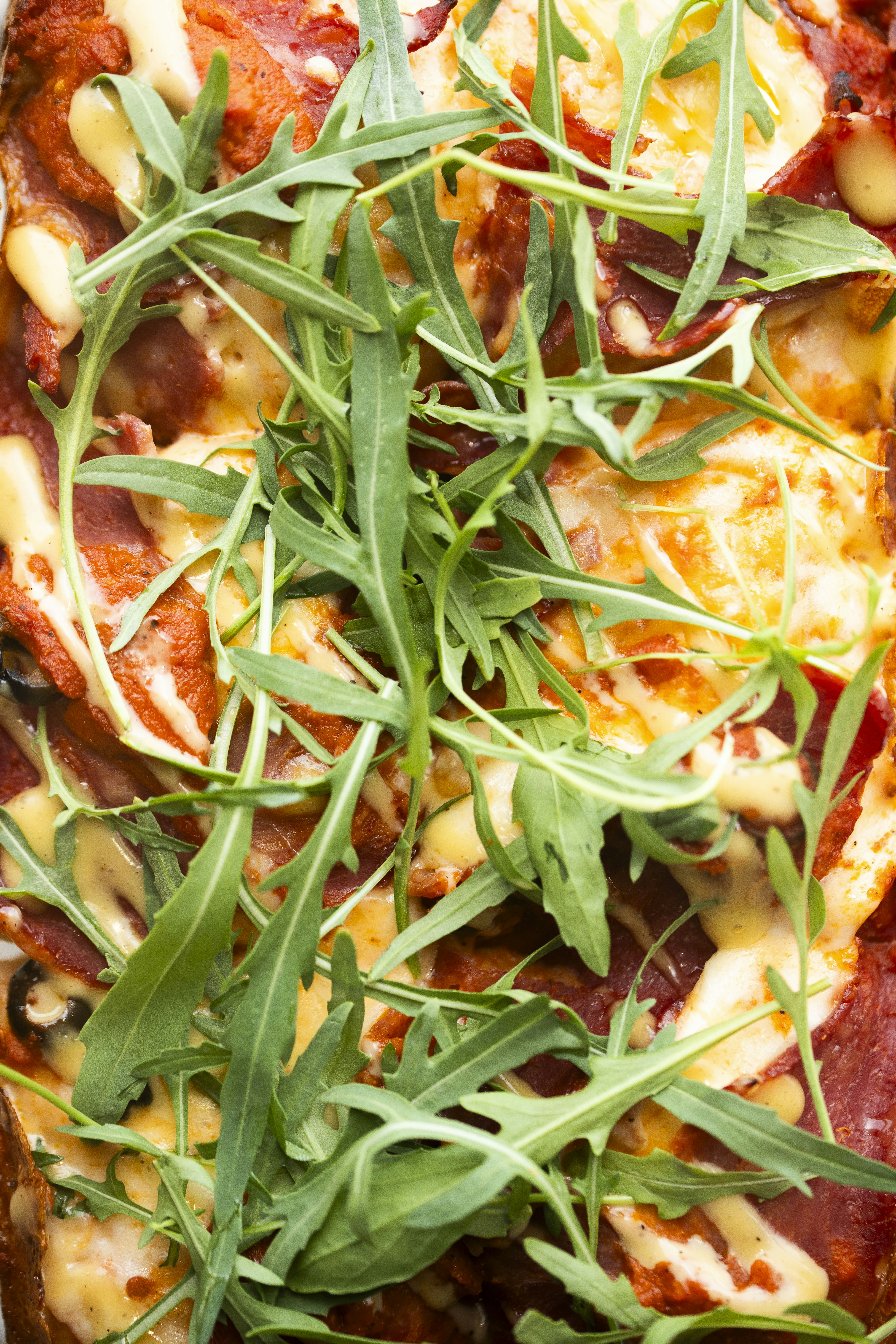 Pepperoni pizza topped with a generous tuft of arugula, molten cheese, and charred edges visible in a close-up shot.