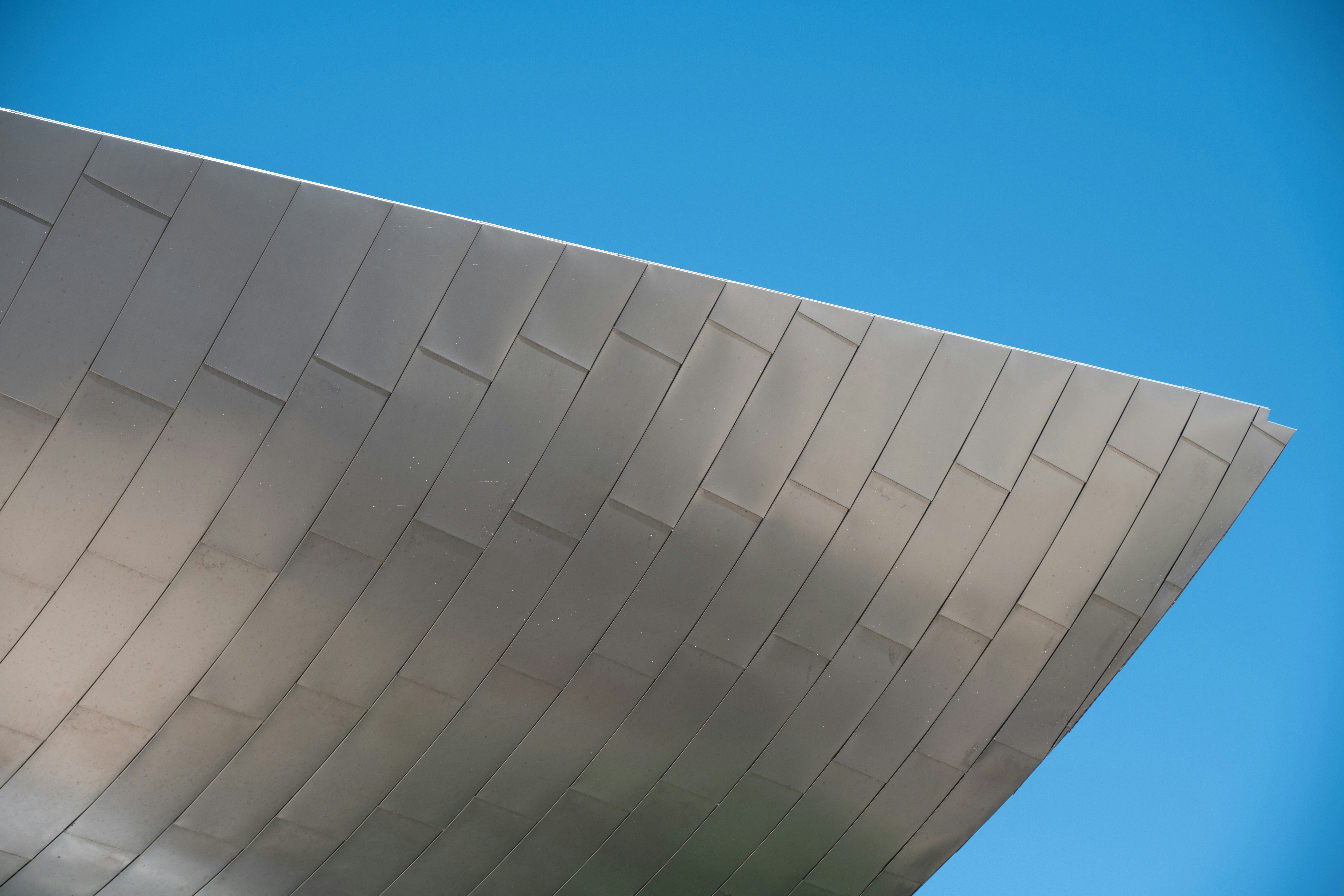 A sharp, metallic paneling angle meets a vivid blue sky, capturing architectural texture and clean geometry.