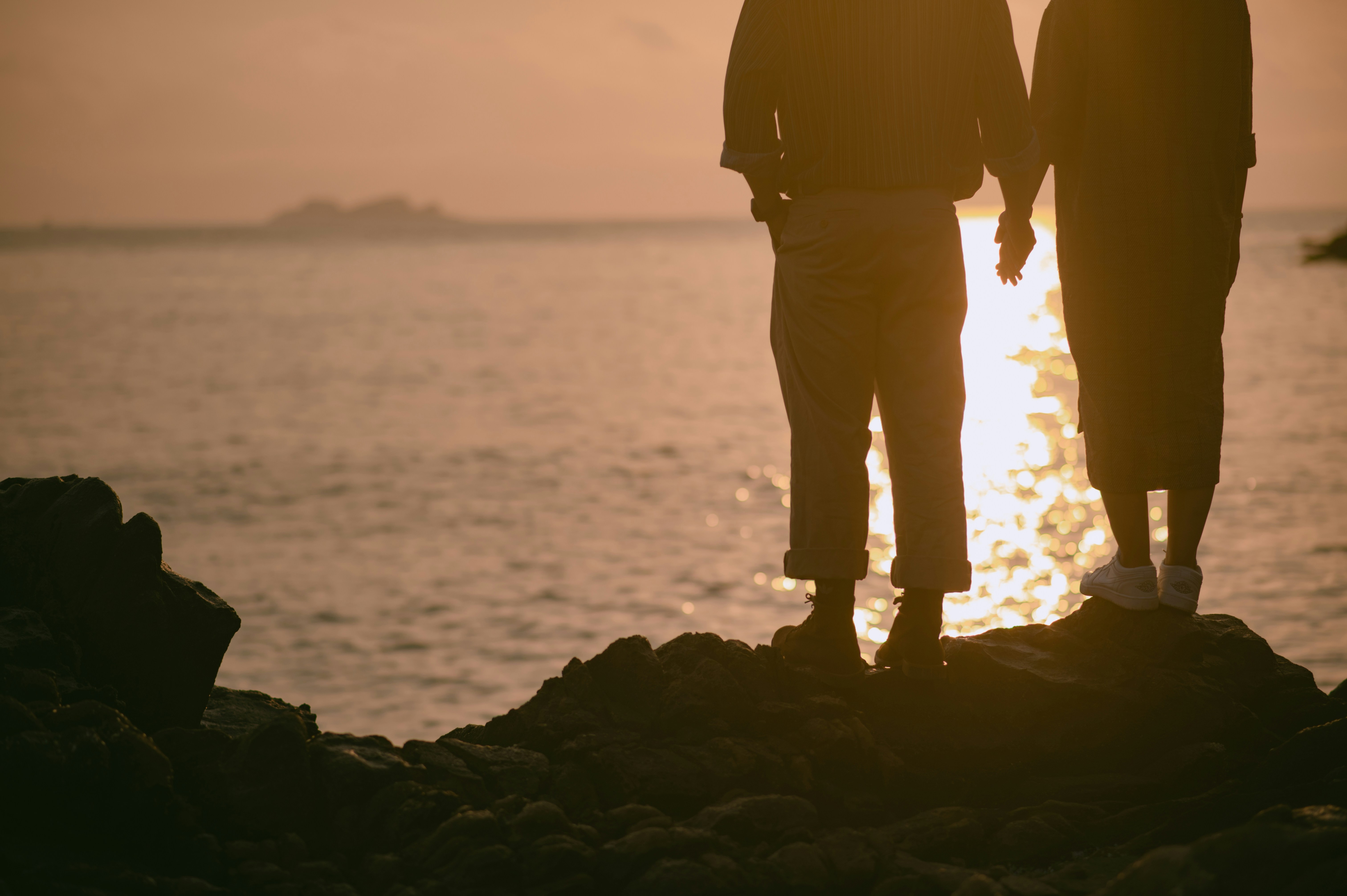 Two silhouettes on a rocky shore at golden hour