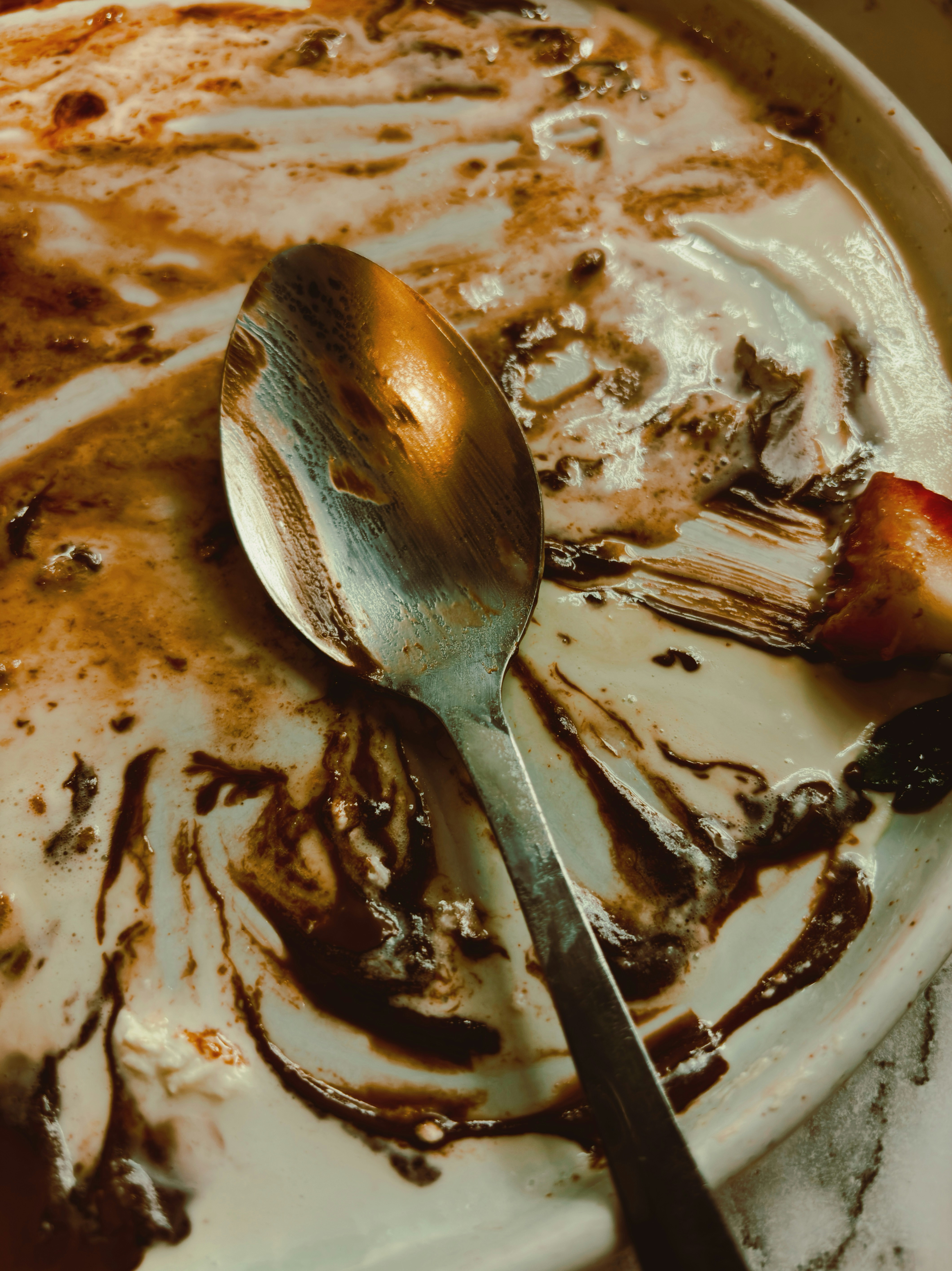 Creamy dessert dish with a metal spoon resting on swirled chocolate and cream textures; a bite reveals layered remnants and a partially visible fruit piece.