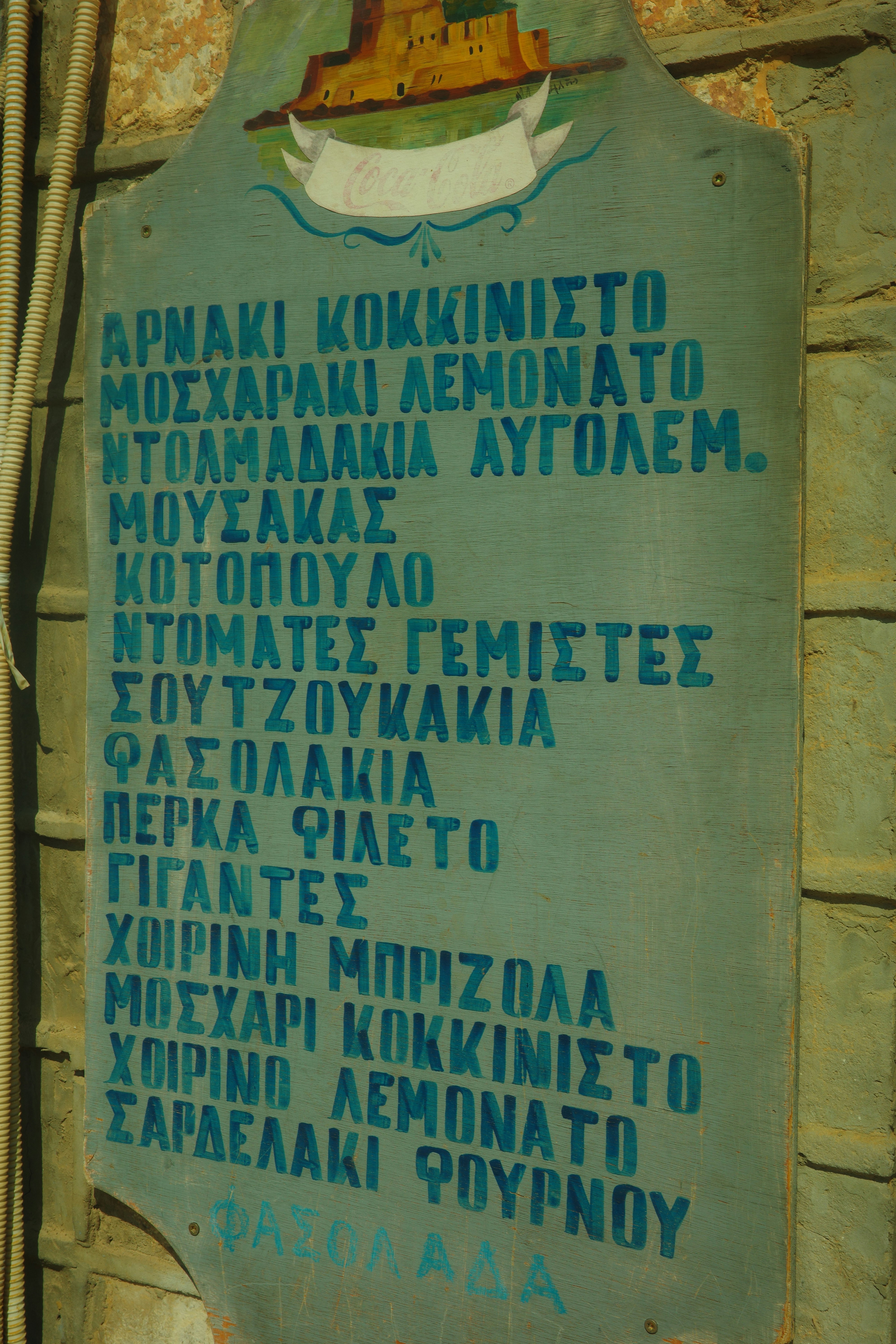 Blue-Greene Signboard with Greek Menu Text in a Rustic Wall Setting