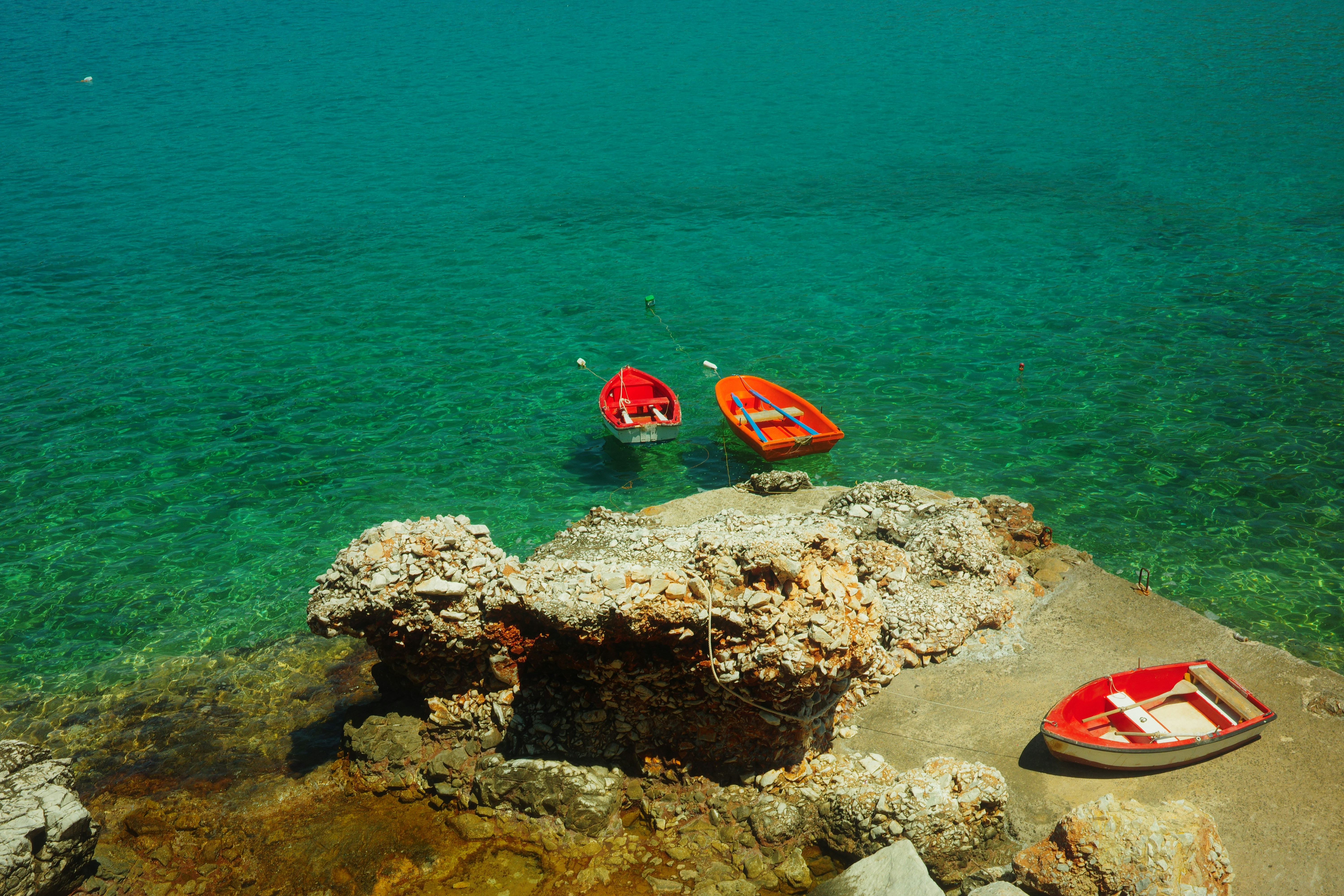 Emerald Waters and Red Boats Resting on Sunlit Rocks
