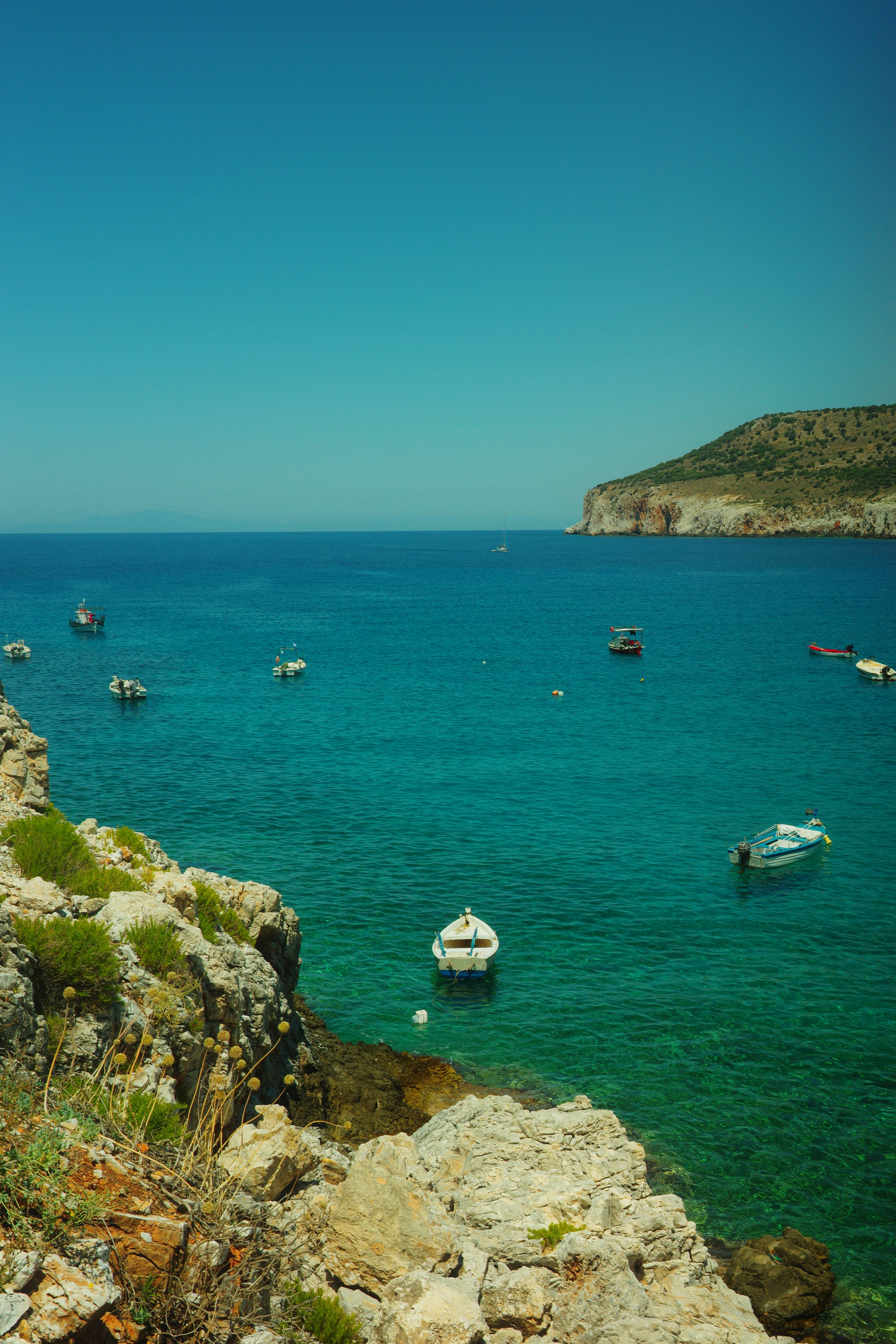 Azure Ledge: Boats Drift in Quiet Sea by Rugged Shoreline