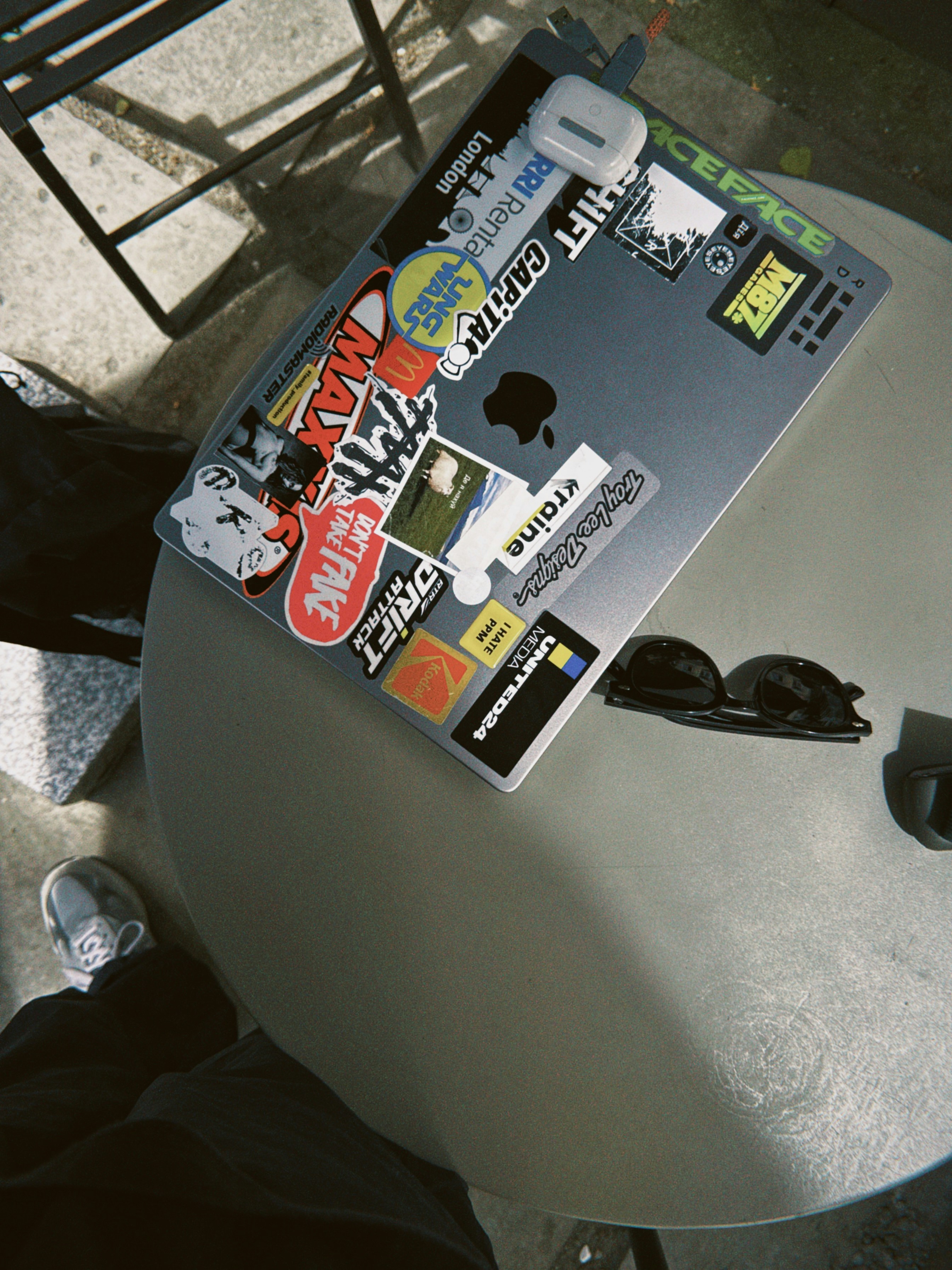 Stickered MacBook on a Round Table Casting Shadowed Confetti of Gear