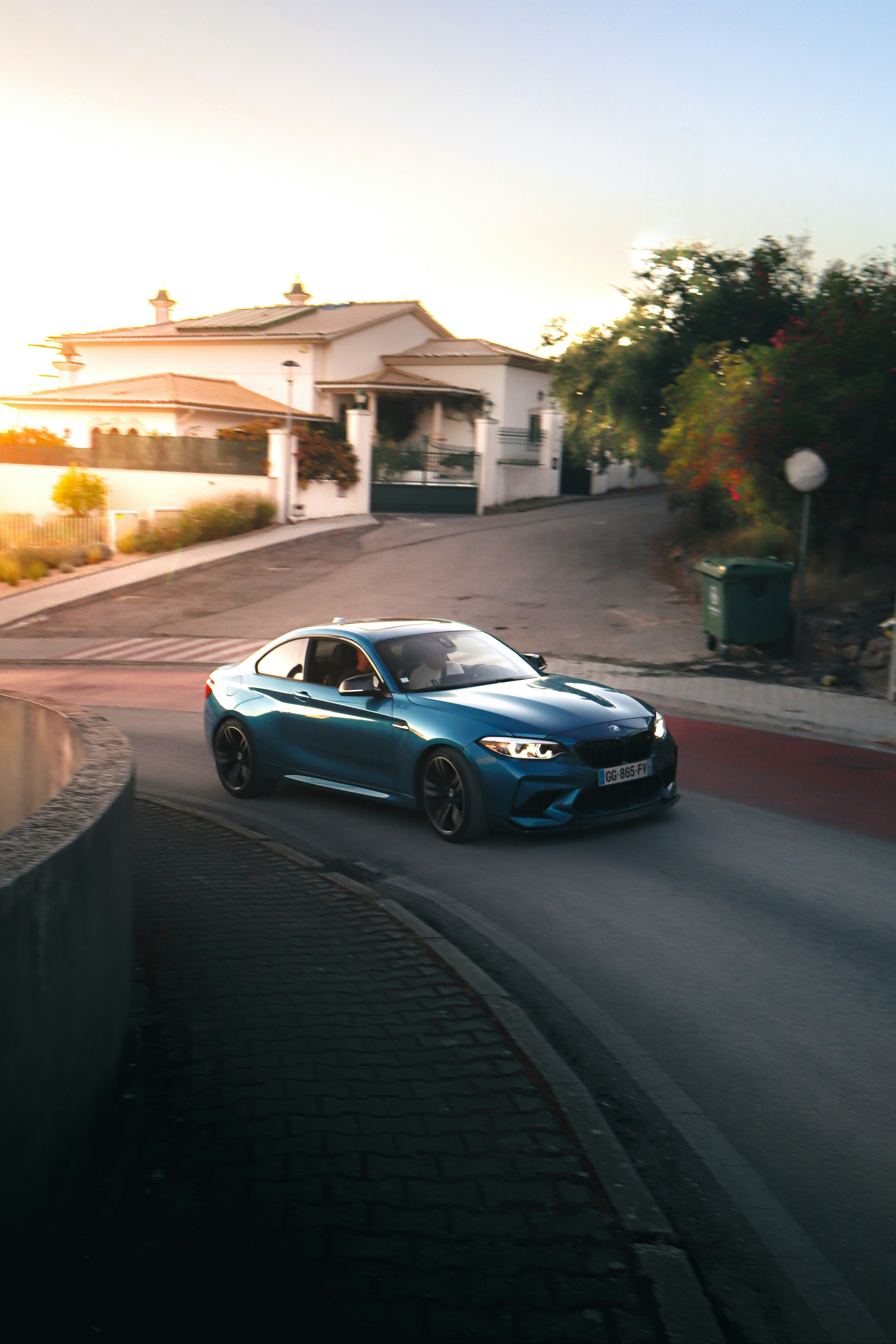 Blue sedan rounds a sunset curve beneath a quiet hillside street