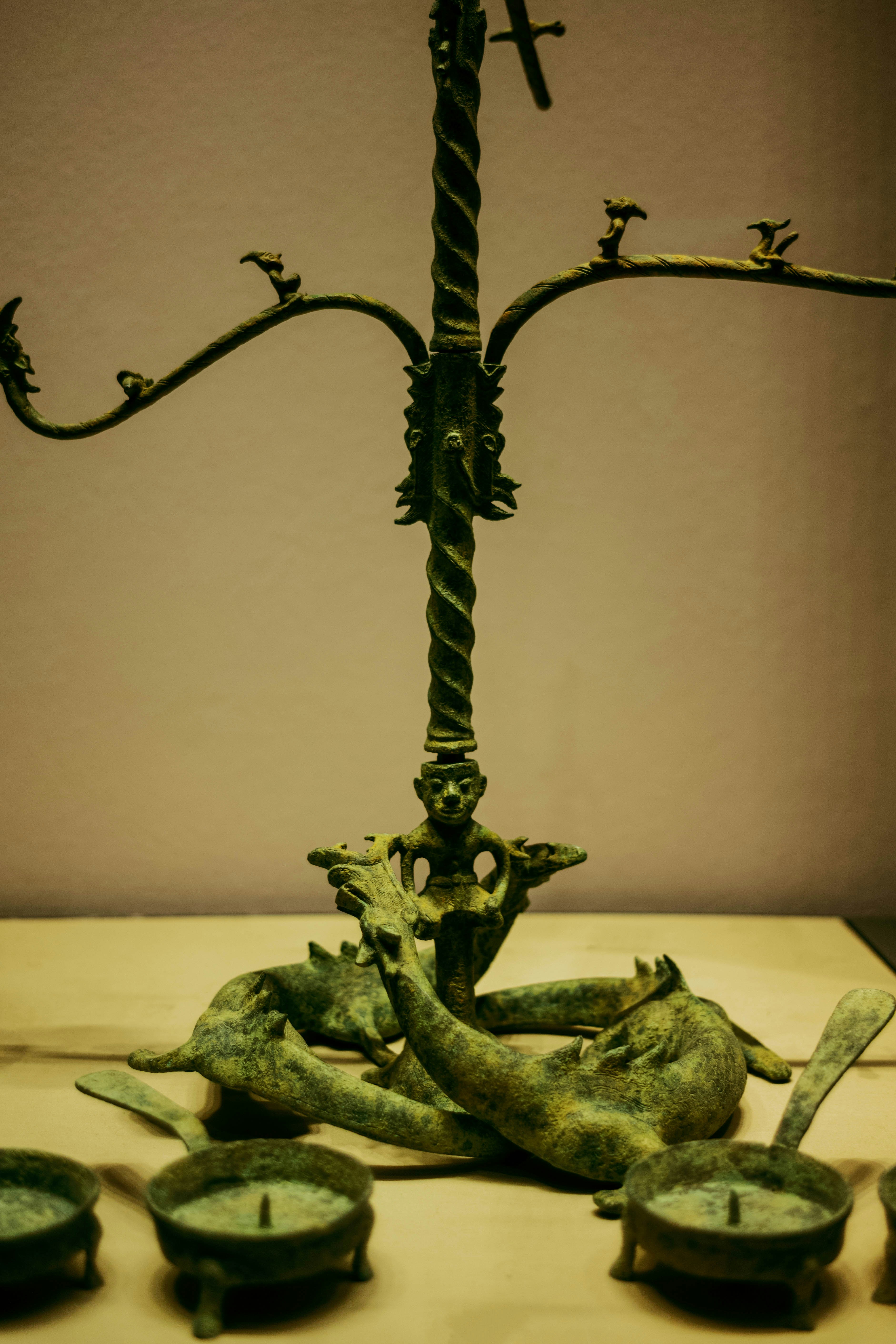 A weathered bronze candelabra with a central figure and coiled dragon base
