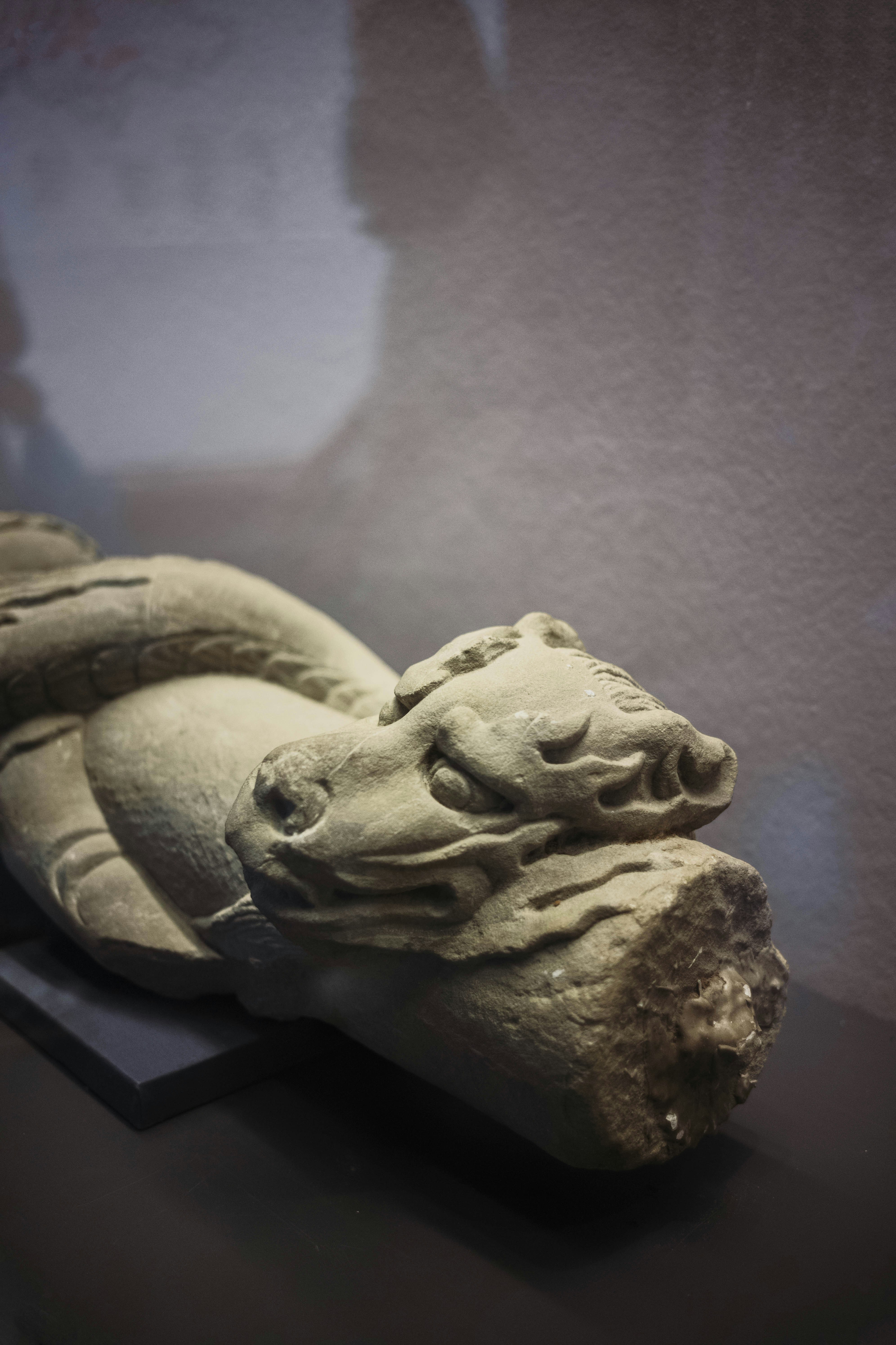 Marble dragon sculpture resting on a dark pedestal, softly illuminated against a neutral wall in a museum setting.