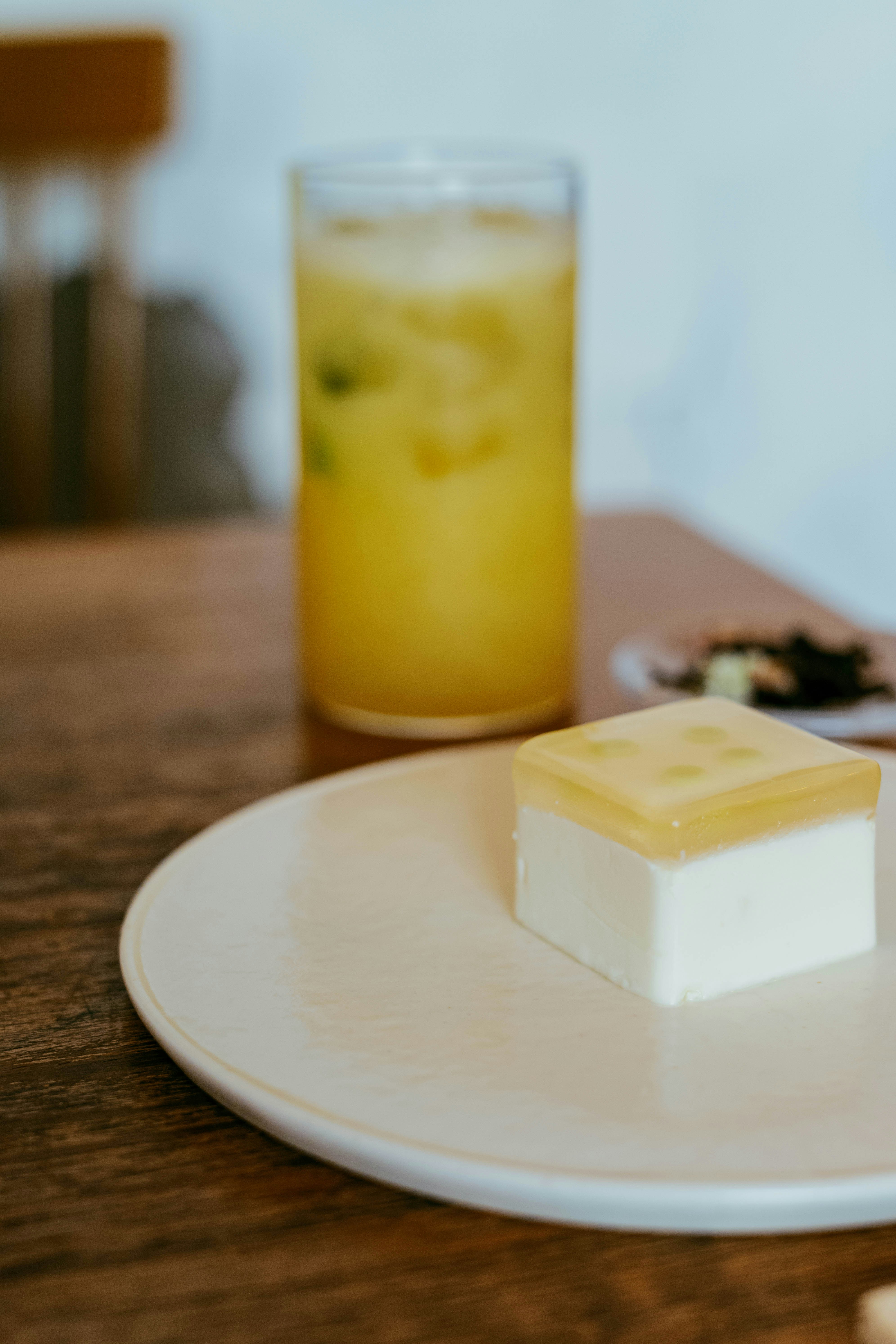 Creamy Cheesecake on a White Plate, with a Glass of Citrus Drink in the Background