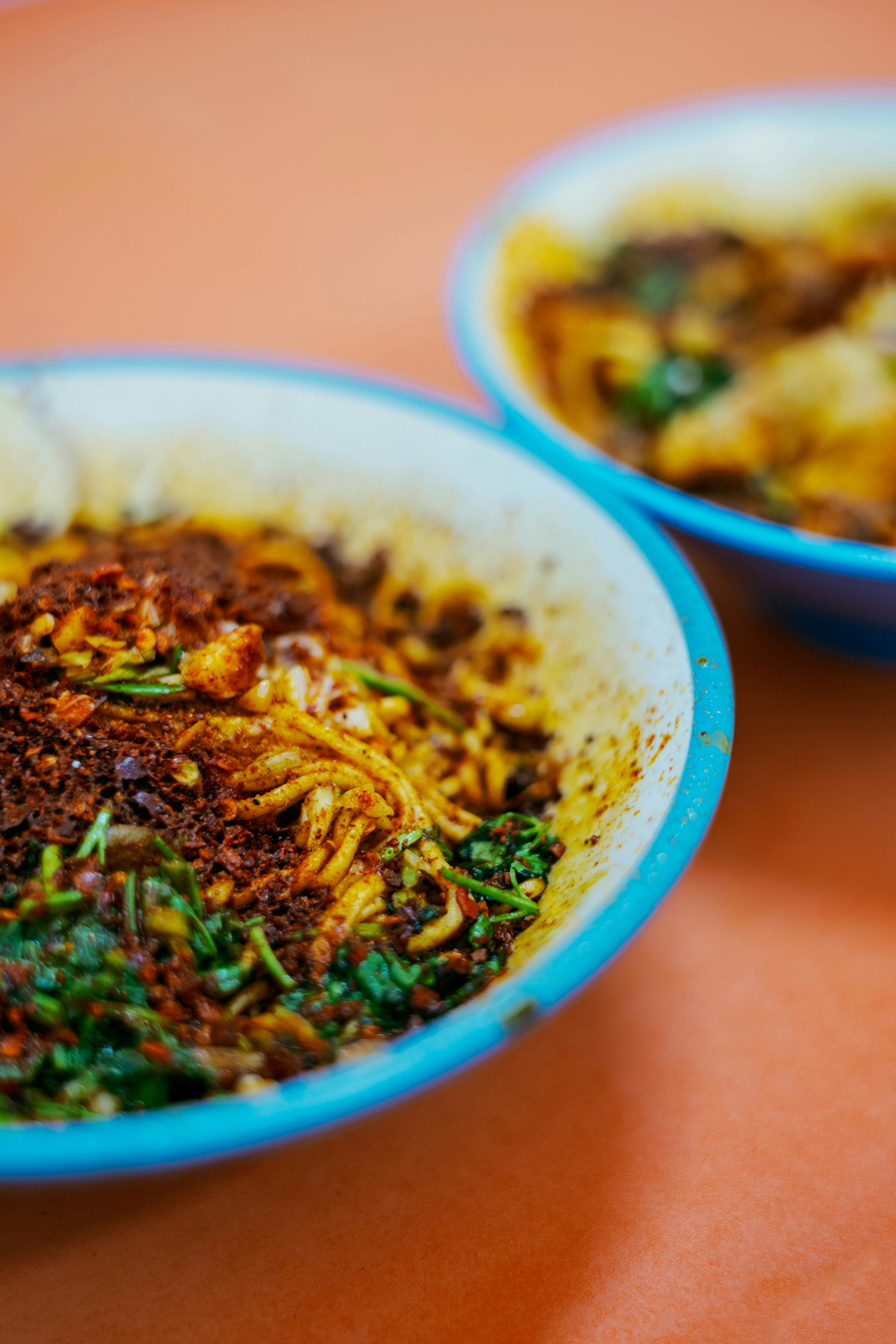 Spiced Noodles in a Blue-Rim Bowl: Close-Up with a Second Dish Fading