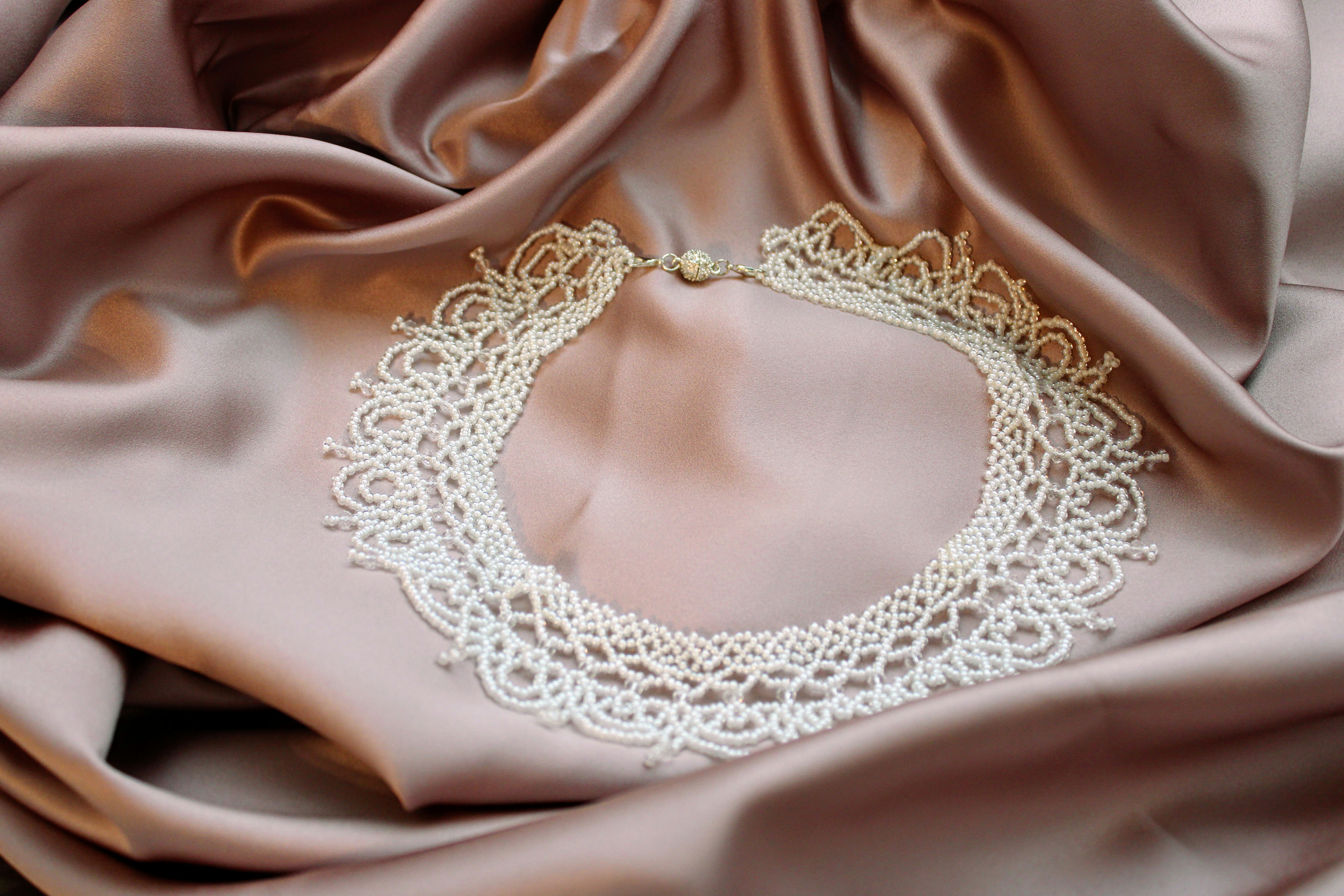 Lace Halo: a delicate white necklace resting on satin folds