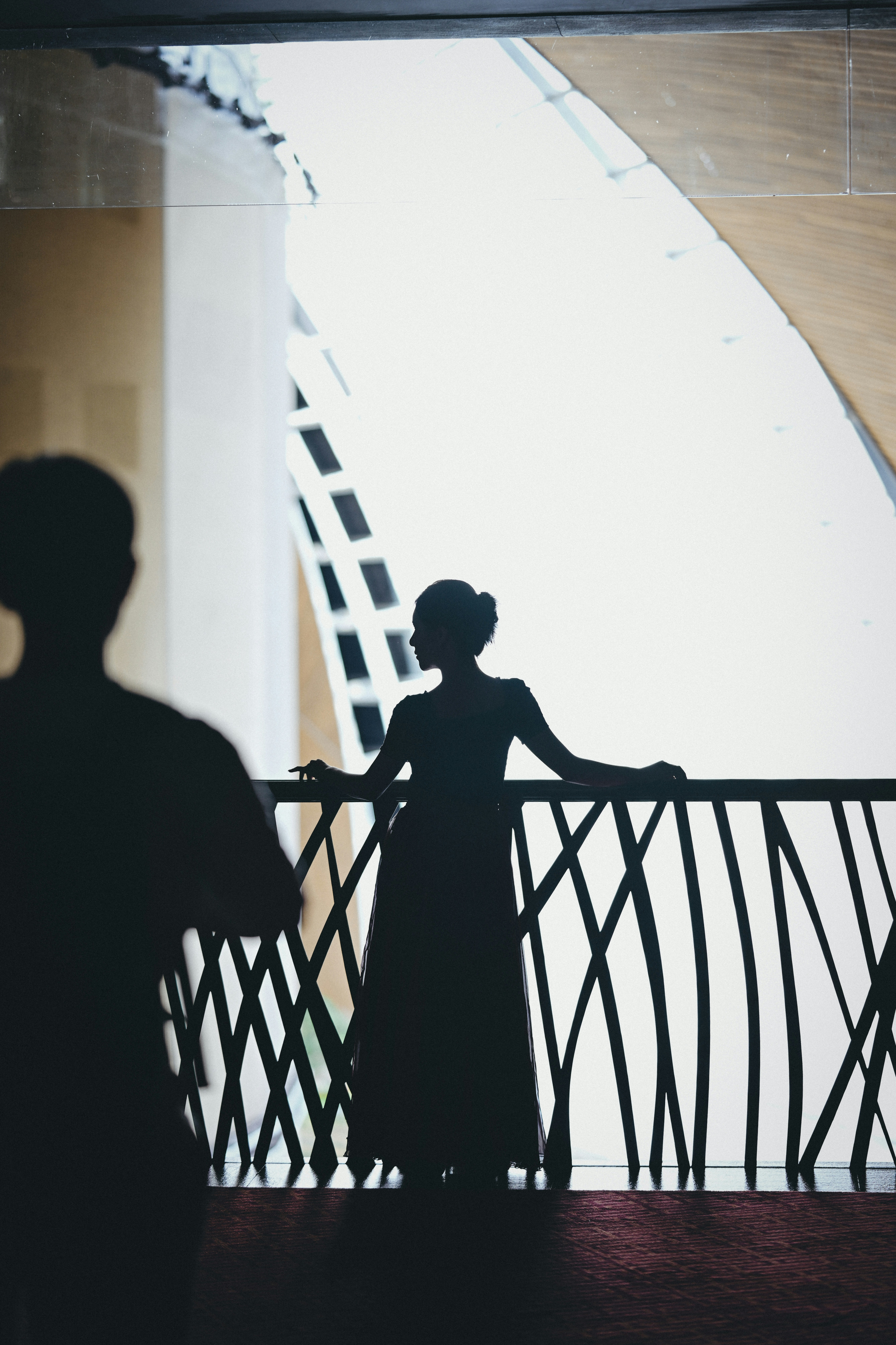 Silhouettes on the Balcony: A Quiet Pivot Over an Illuminated Atrium