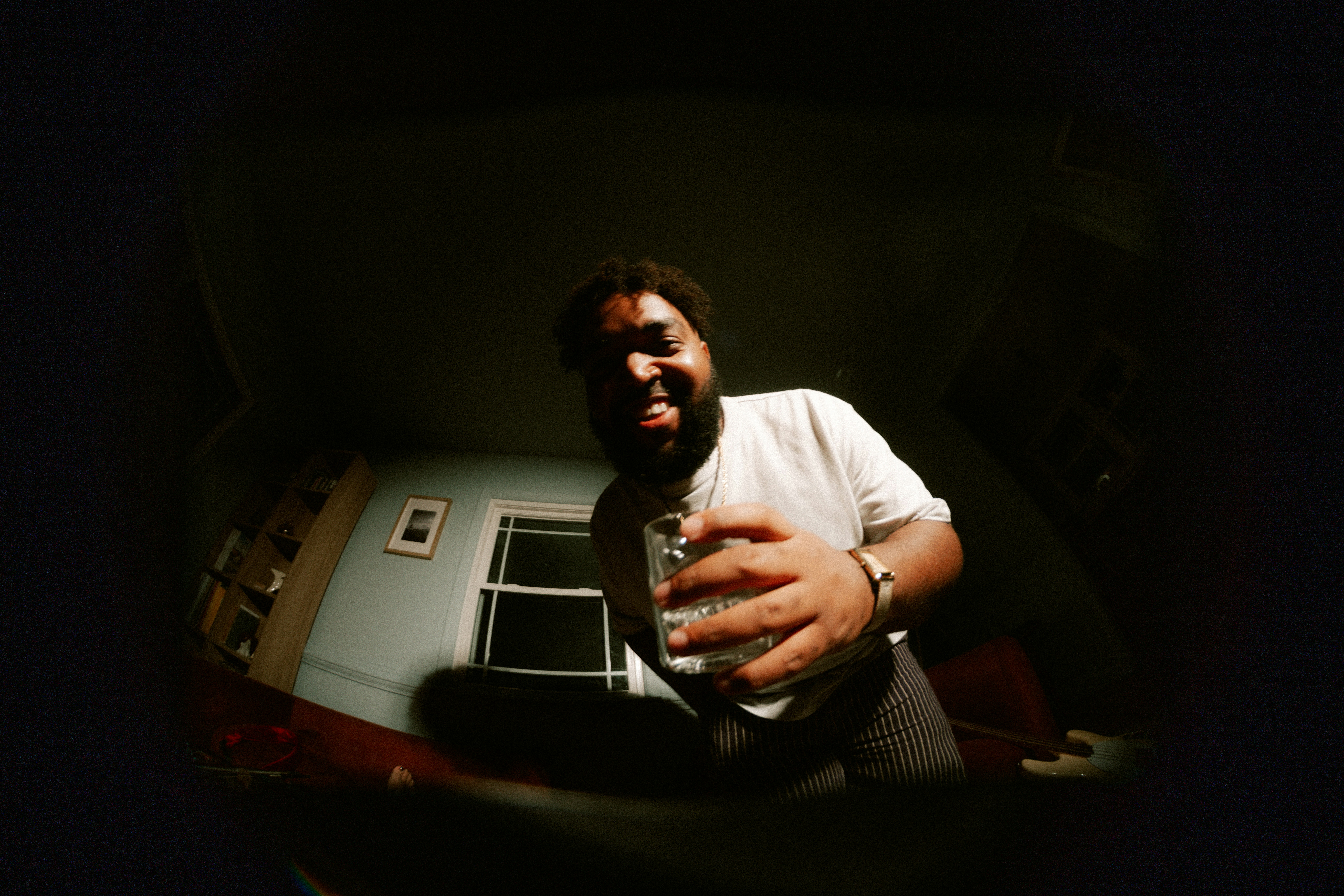 Close-up in a Wide Lens Moment: The Welcoming Grin and Glass in a Dim Kitchen