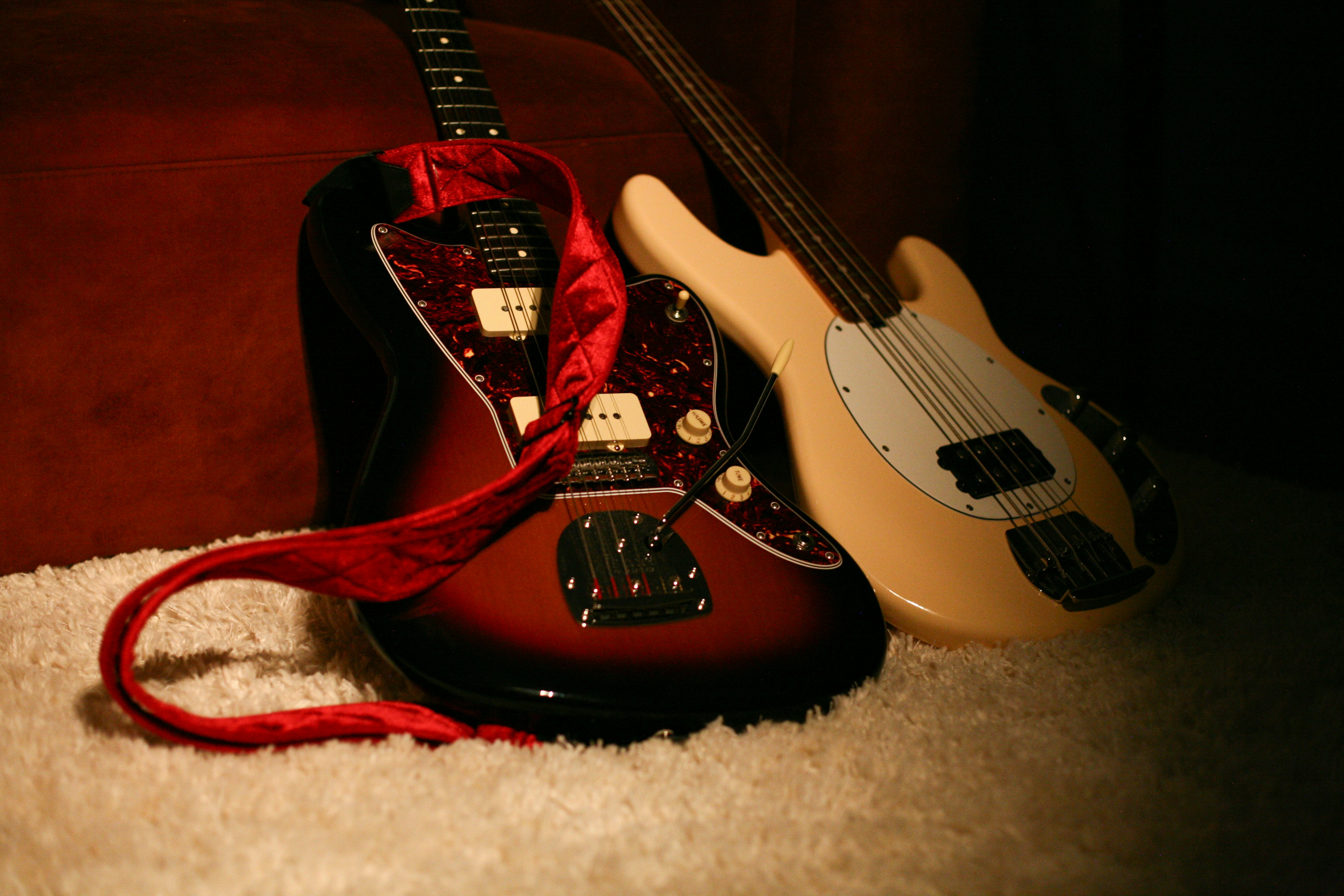 Red Strap Quietly Anchors a Pair of Guitars in a Dim Corner