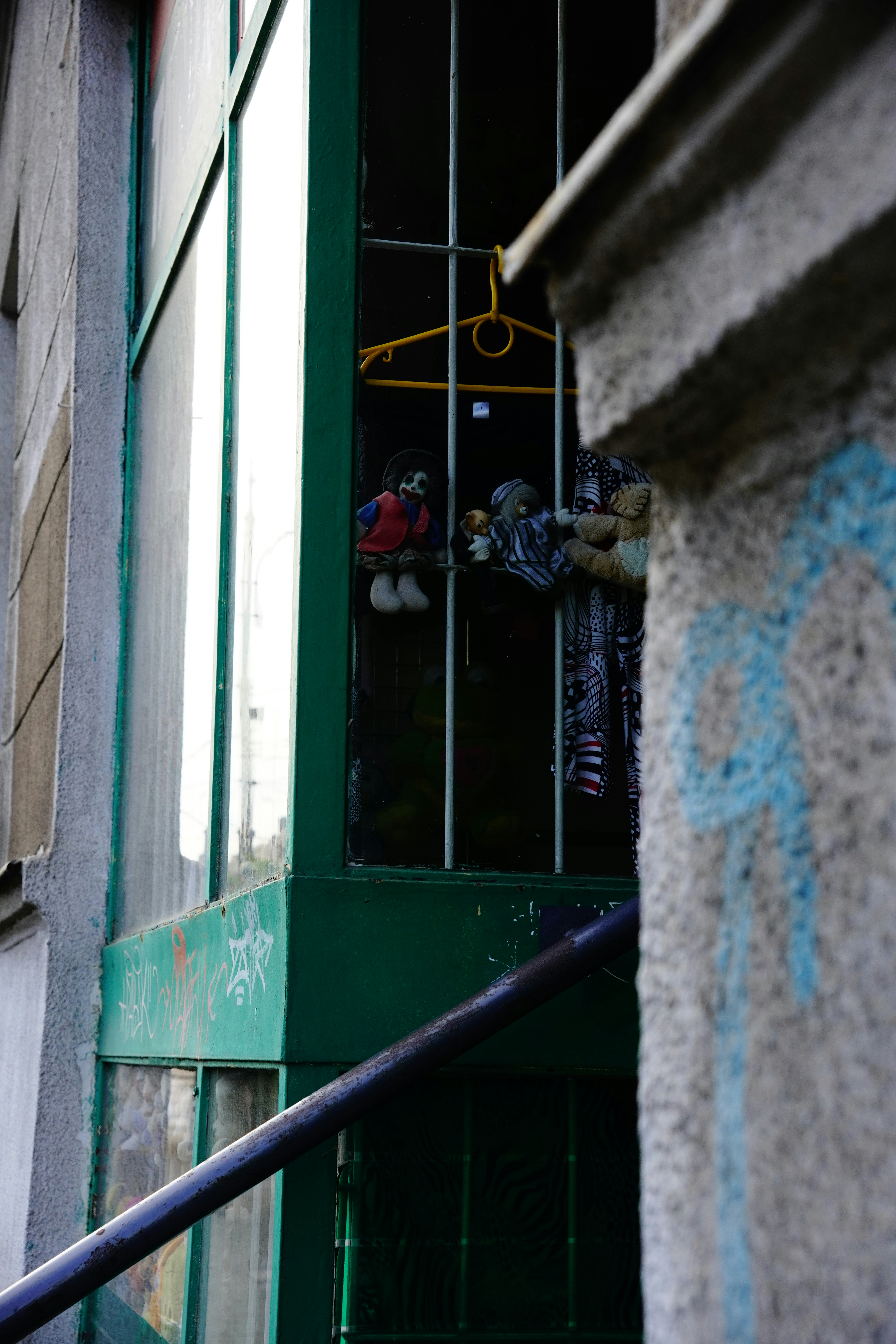 Green storefront window with toys behind bars framed by urban walls