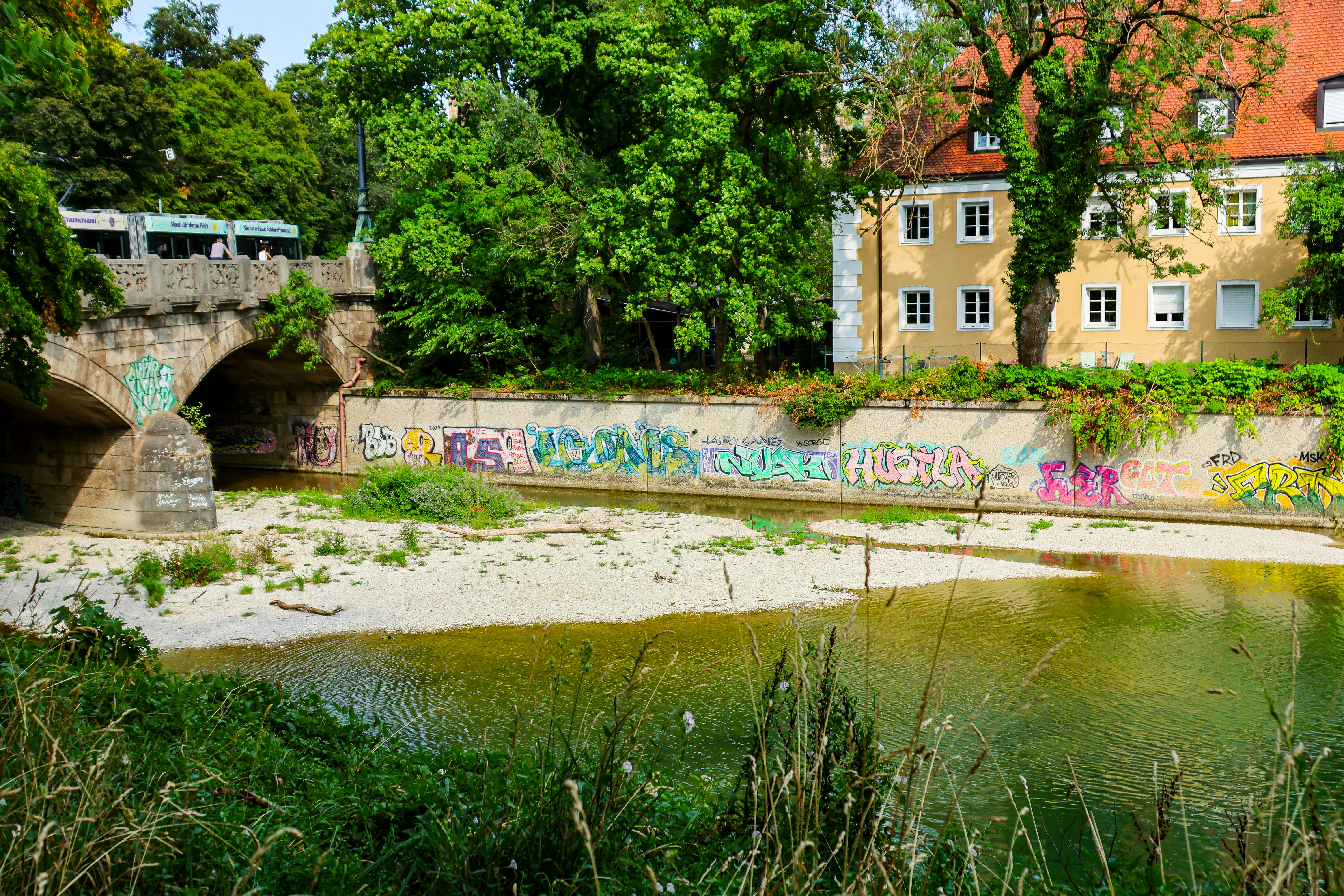 Graffitied riverside wall beside a sunlit European buildingscape