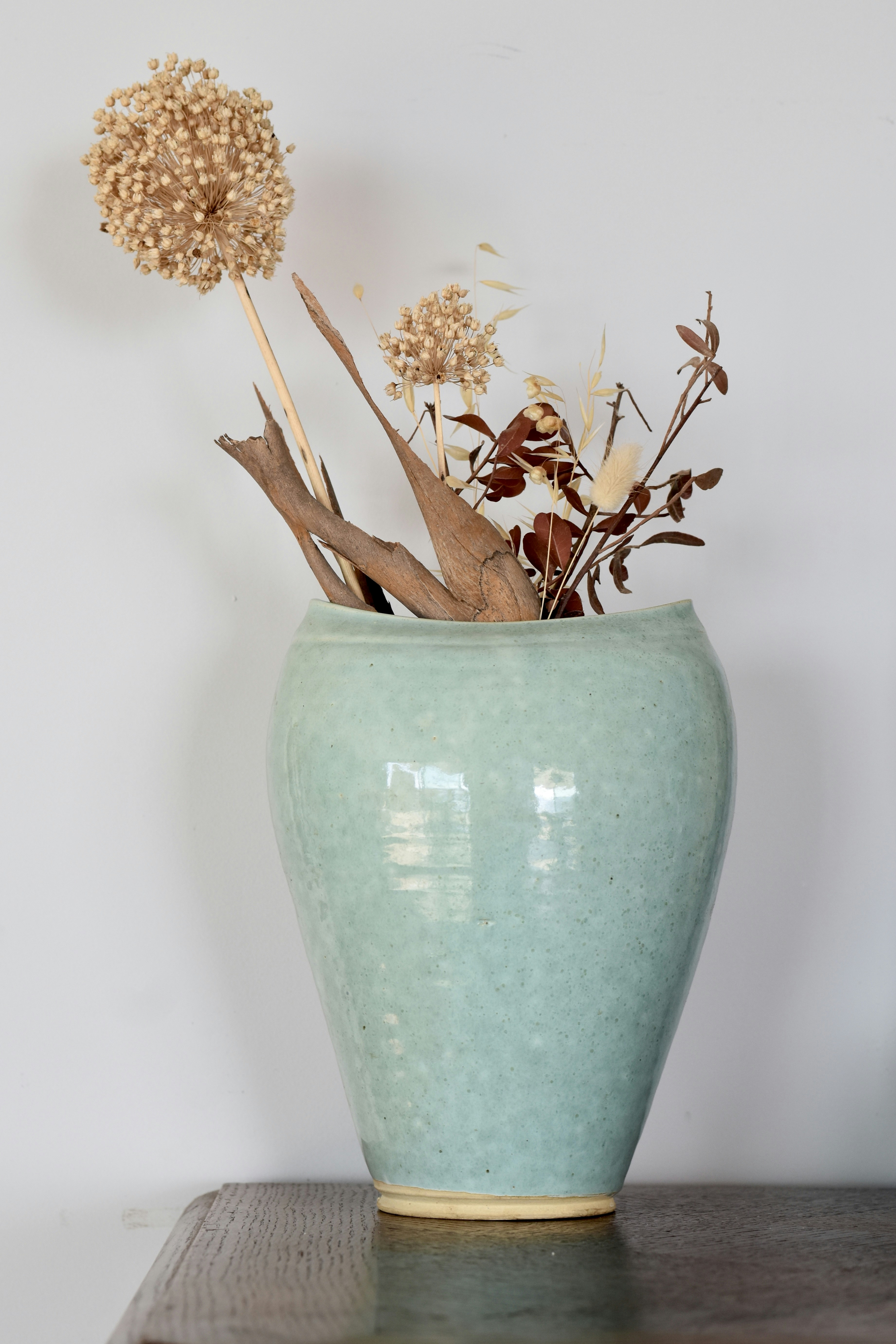 Sculpted Stillness: A Teal Vase with Dried Sprigs on a Wooden Table