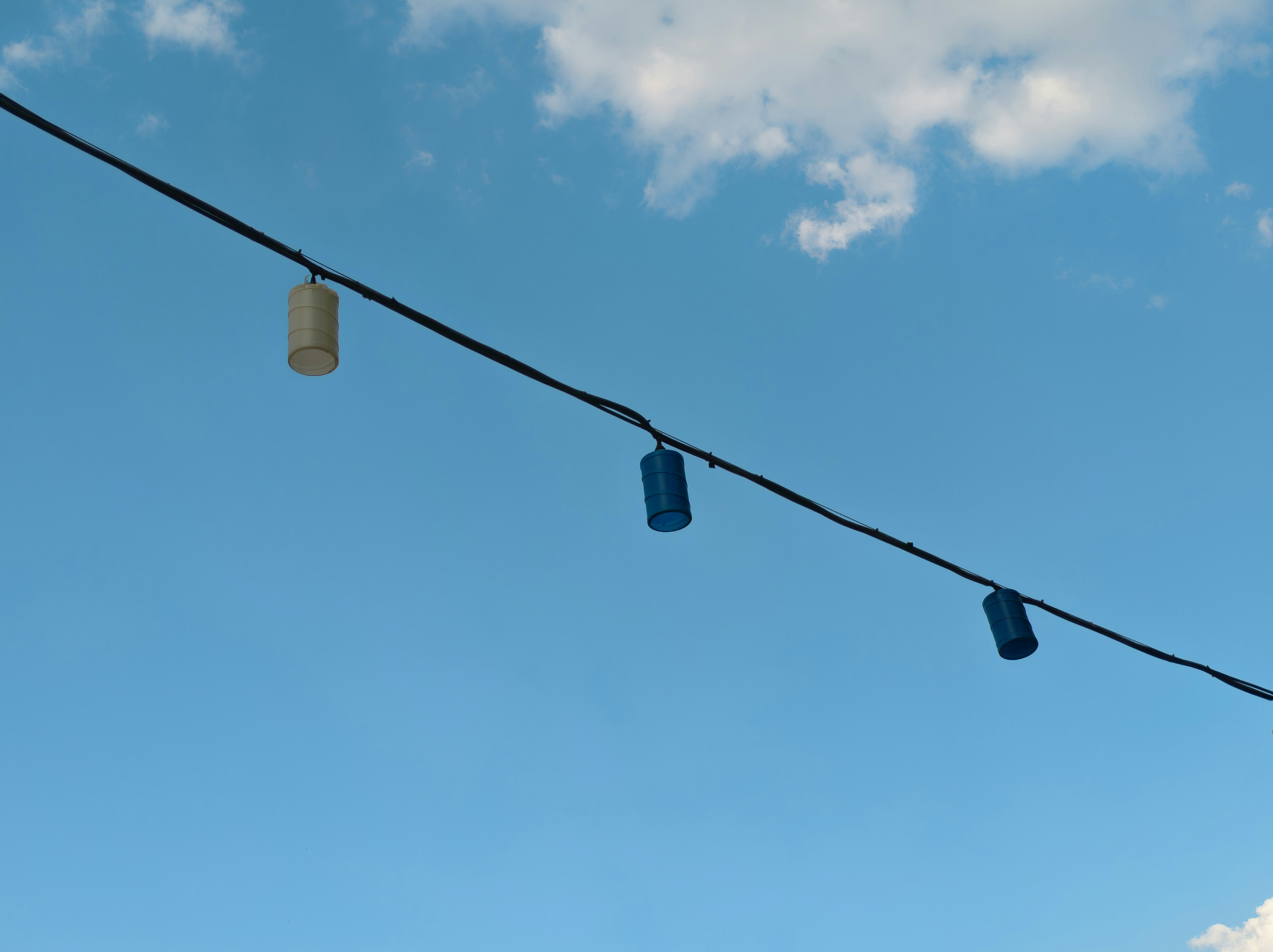 Three cylindrical lanterns hanging from a wire against a bright blue sky.