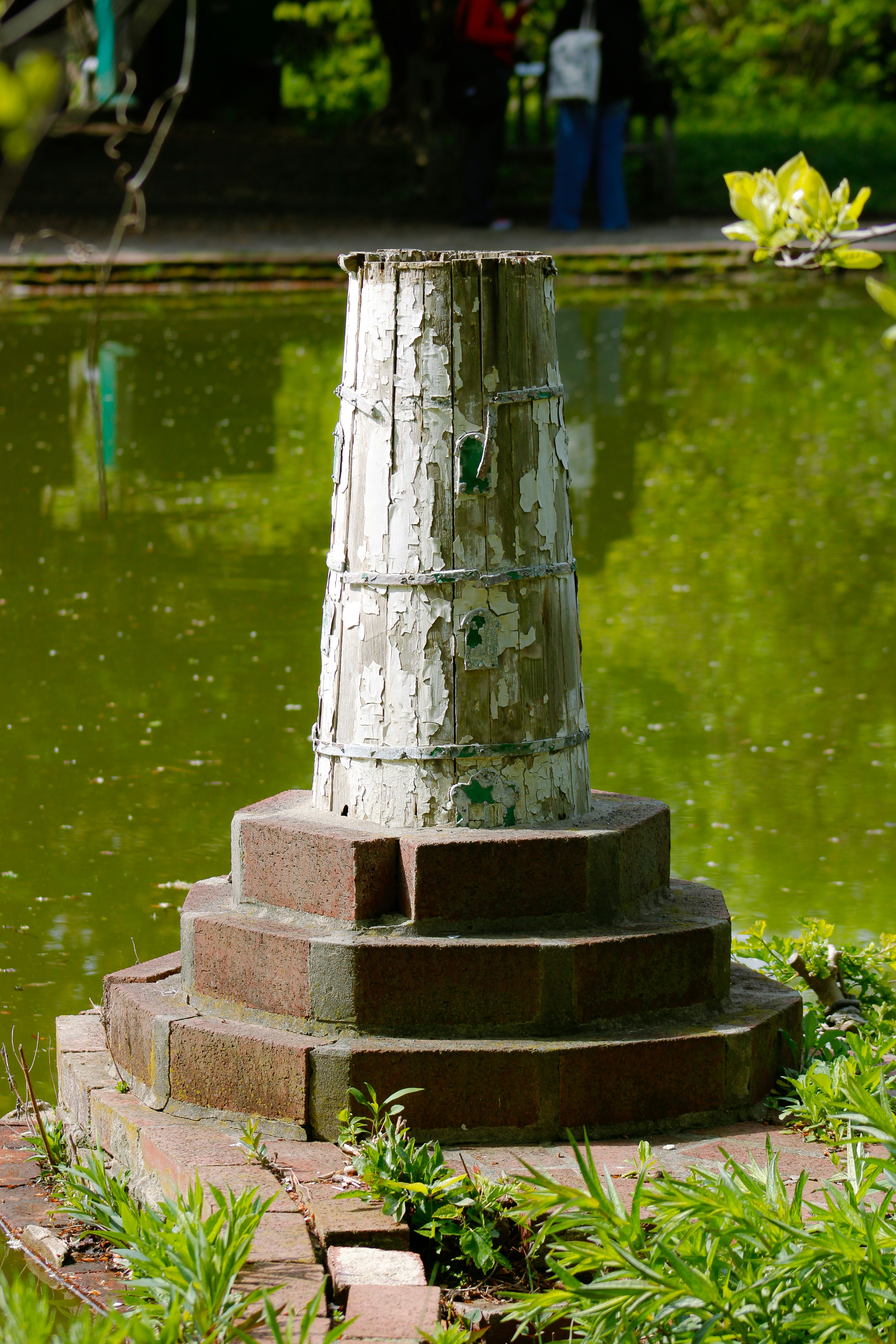A weathered wooden post with peeling white paint on a tiered brick base