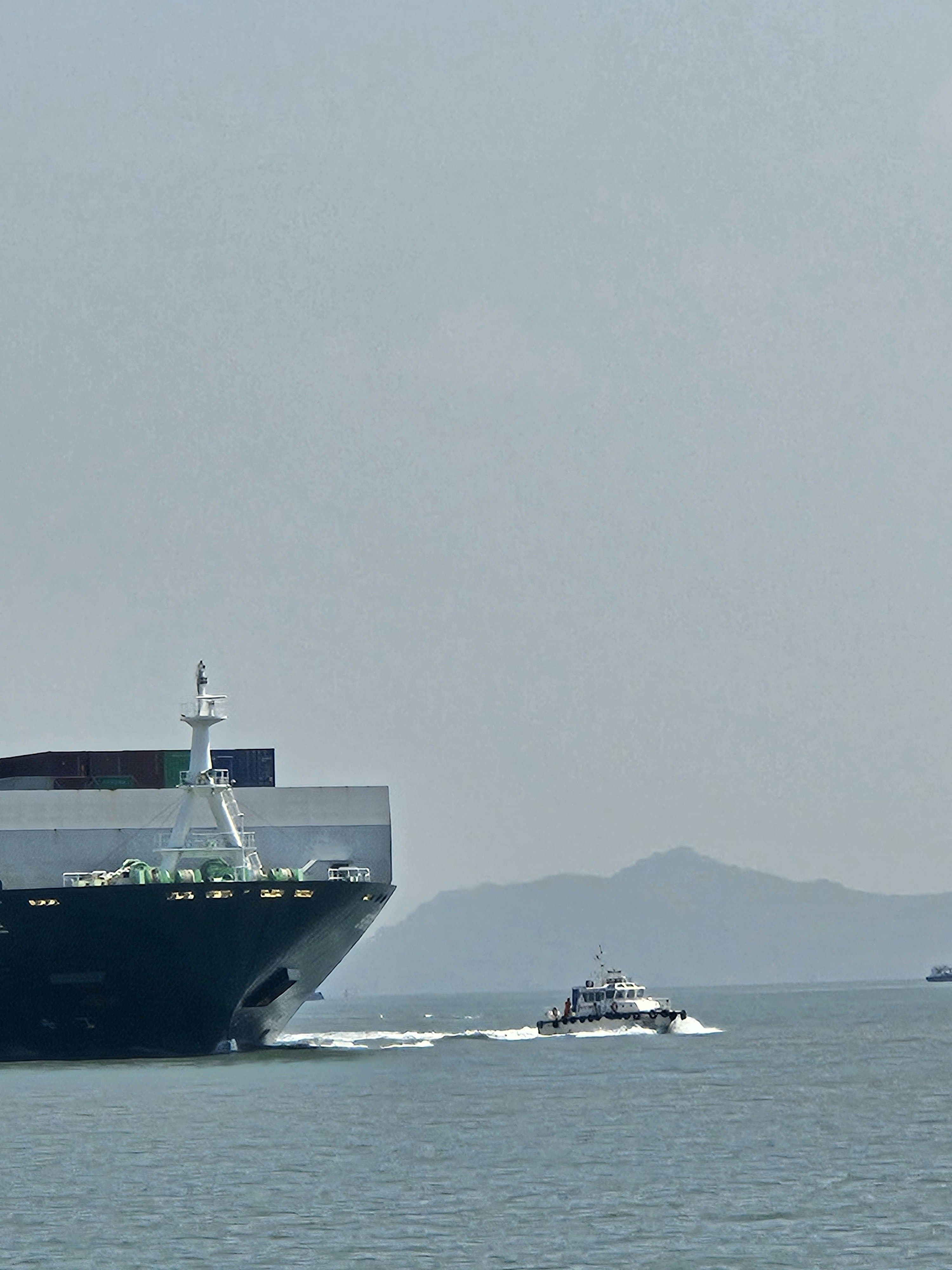 Port-side Giant: A Container Vessel Leads the Quiet Sea with a Small Tug in Tow