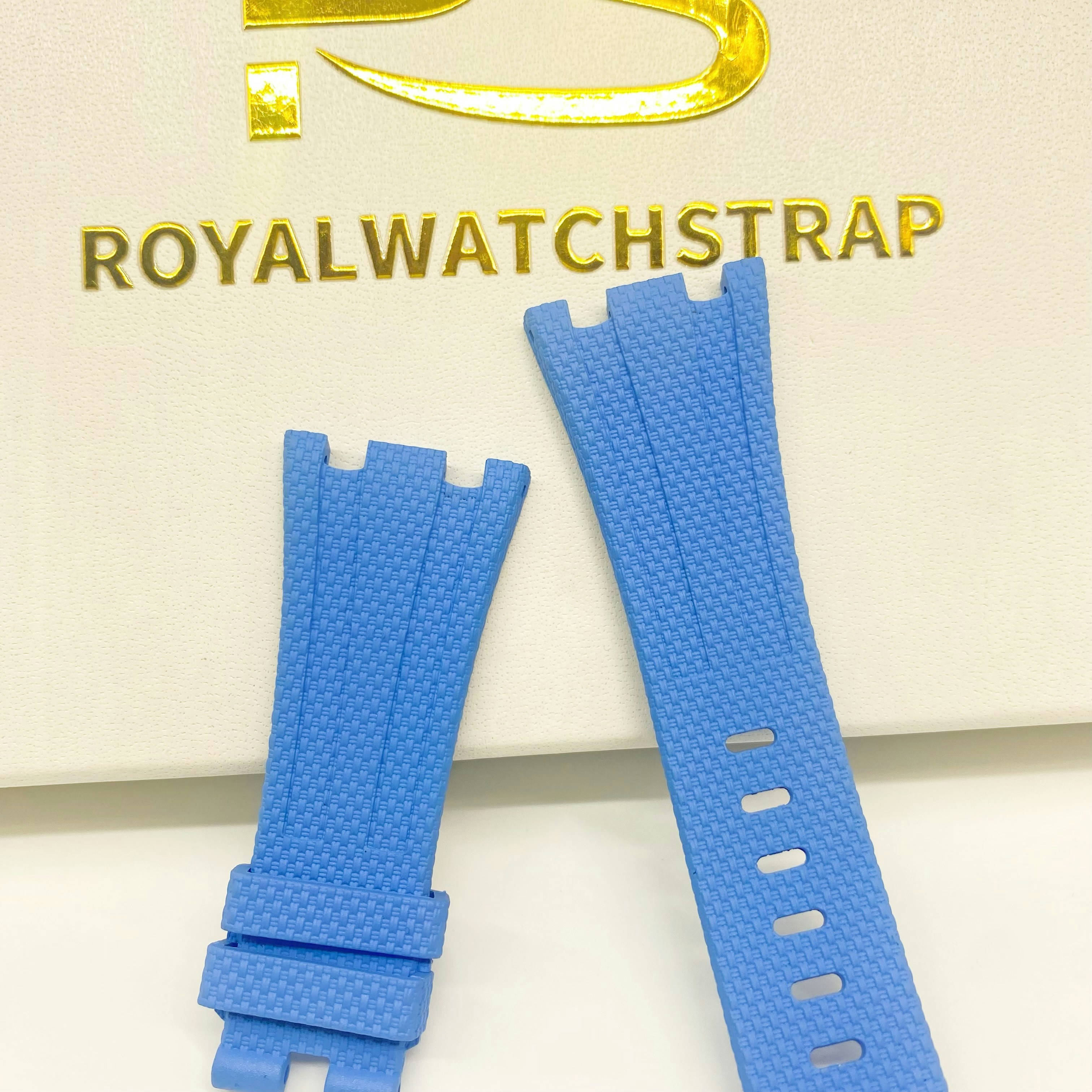 Blue silicone watch straps folded on a light surface beneath a gold RoyalWatchstrap logo.