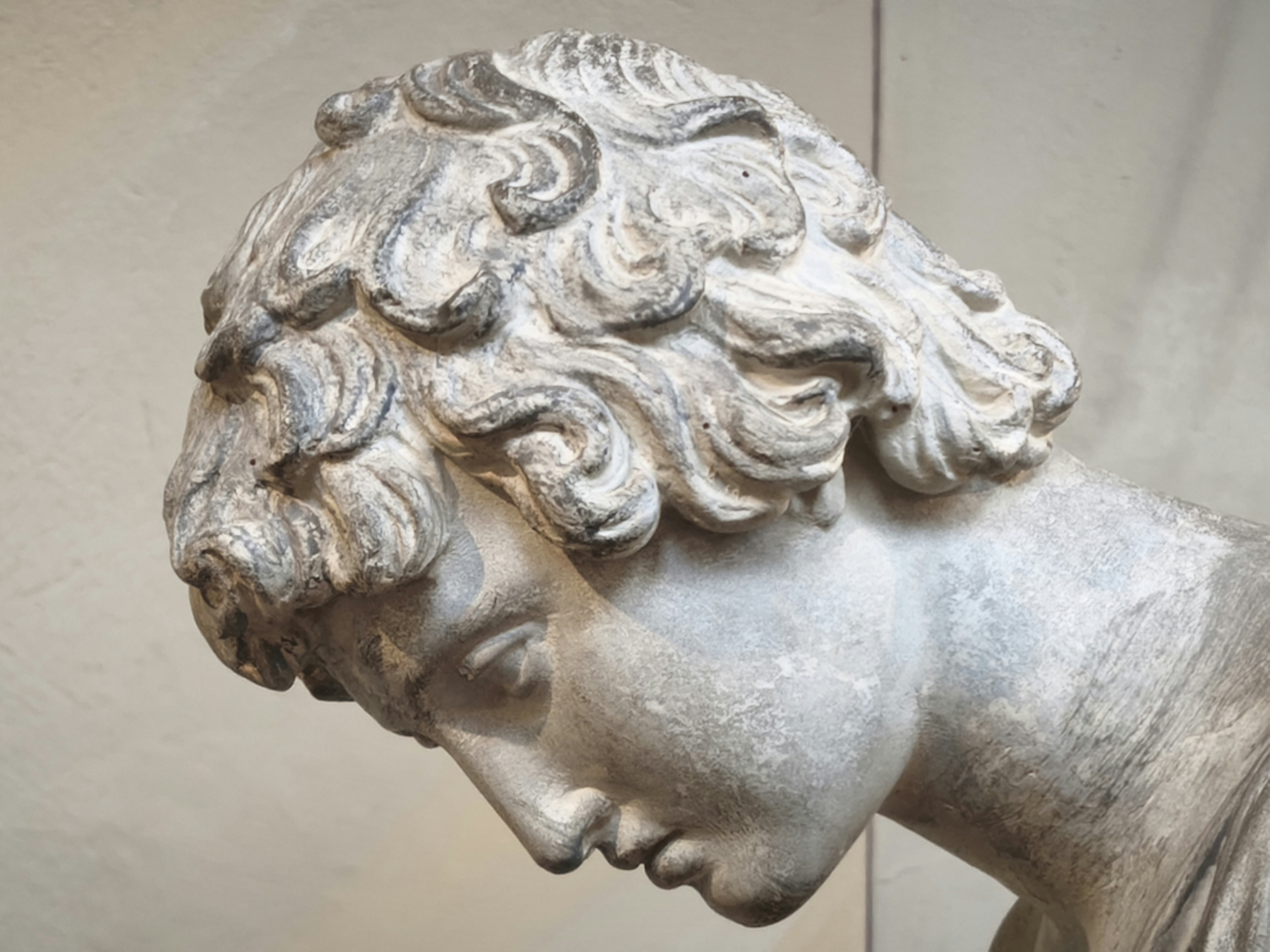 Stone bust of a contemplative figure rendered in soft light, highlighting delicate facial contours and curly hair on a neutral backdrop.